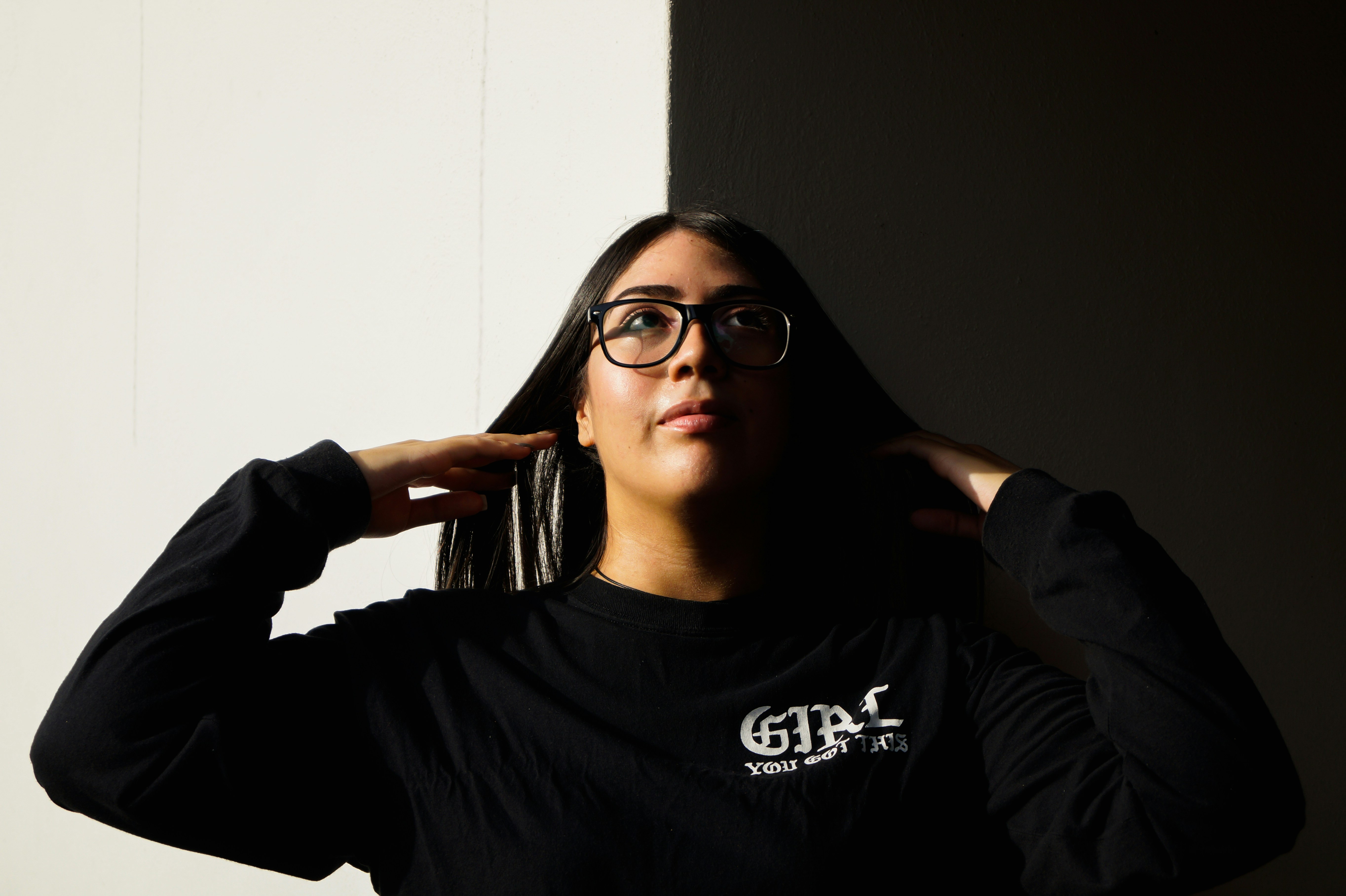 Woman with glasses touches her hair, standing against a stark black-and-white background.