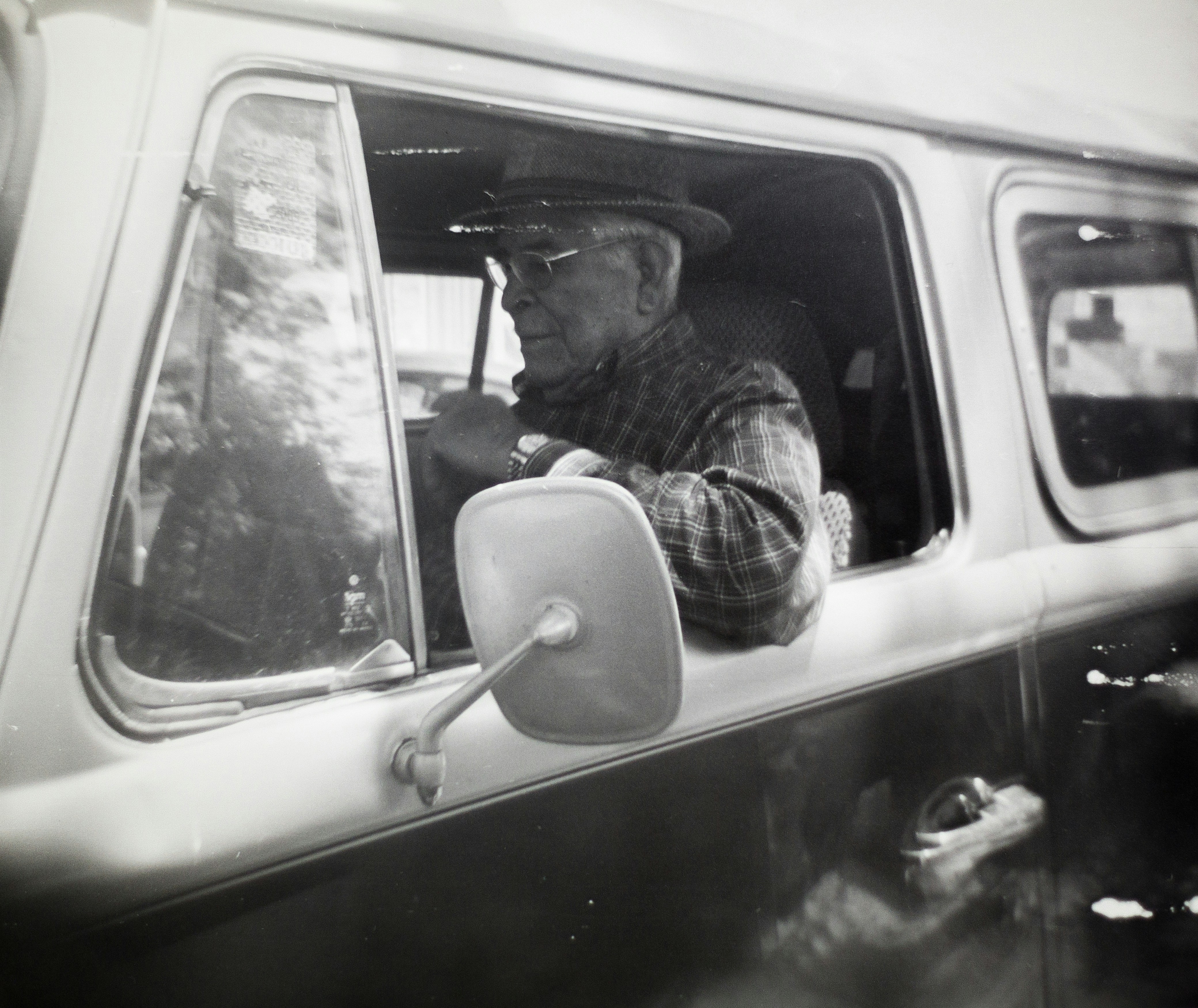 Elderly man sitting inside a vintage Volkswagen bus, wearing a hat and flannel shirt.