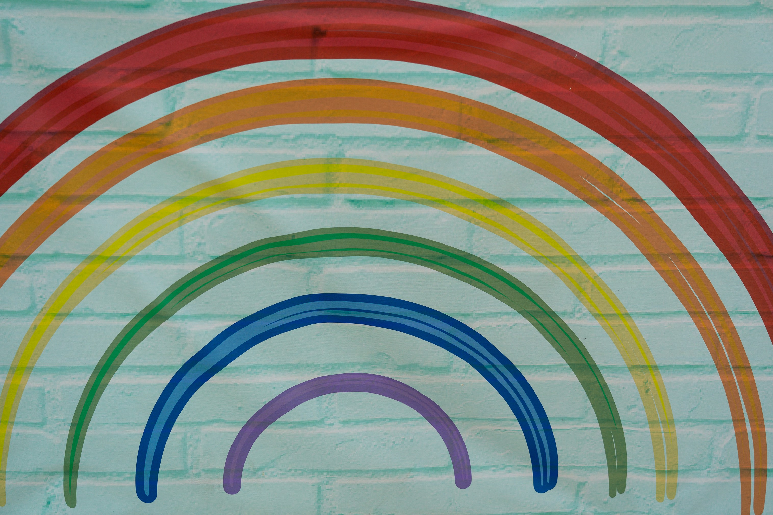 Vibrant rainbow arcs painted on a textured light blue brick wall, showcasing a spectrum of colors from red to purple.