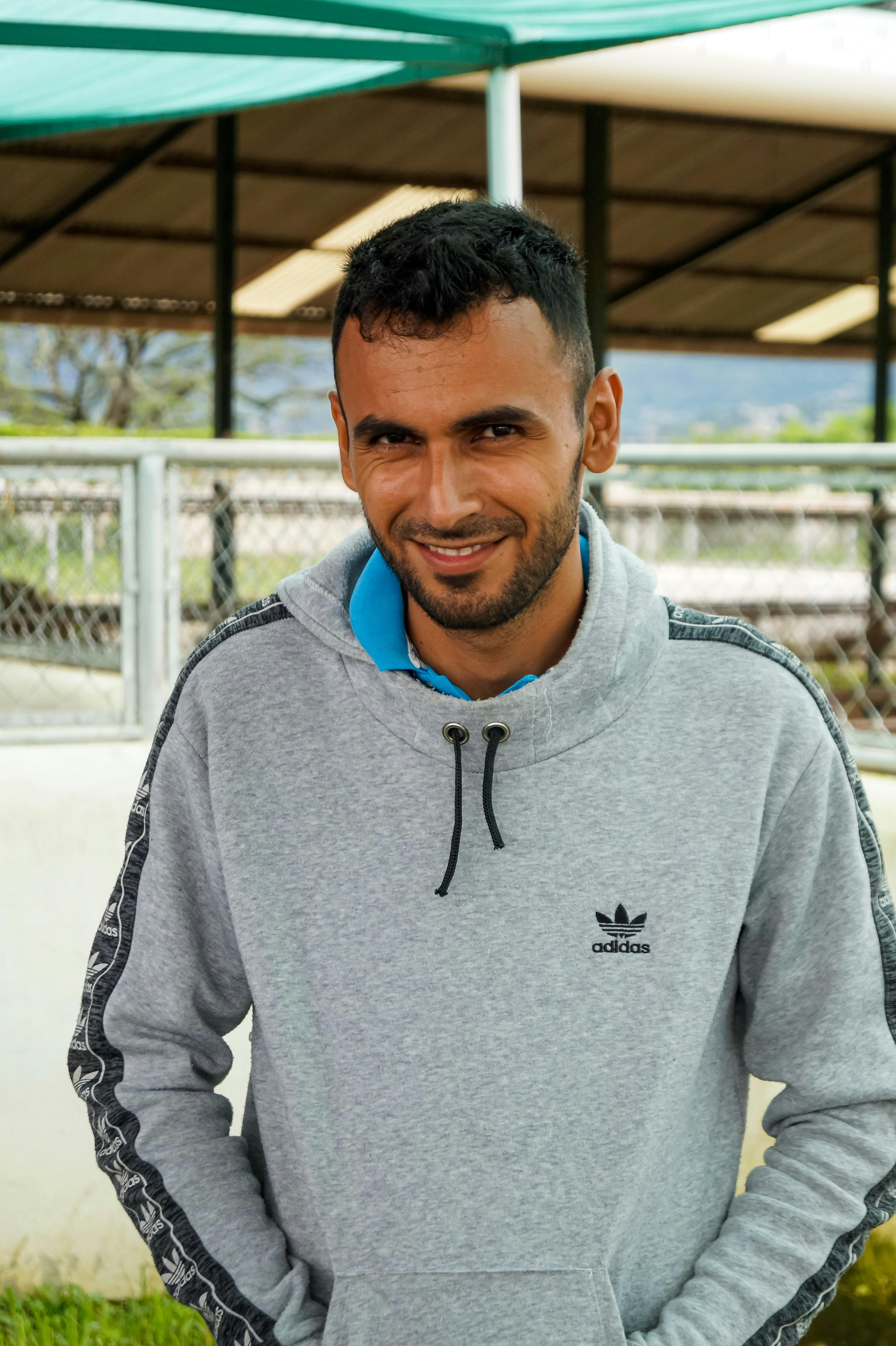 Man in a grey hoodie stands outdoors with a relaxed expression.