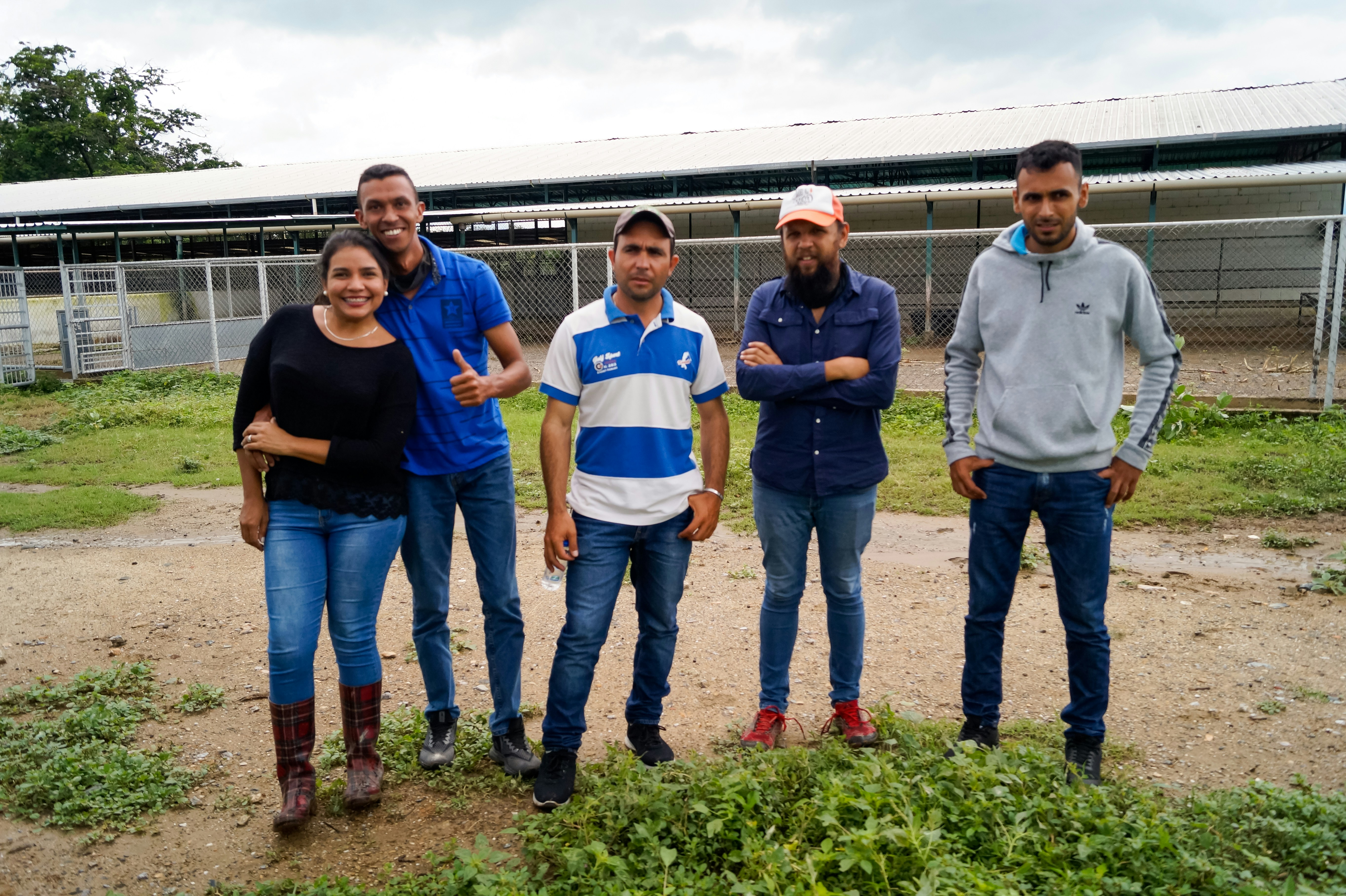 Group of five people standing outdoors on a grassy area with a long building in the background.