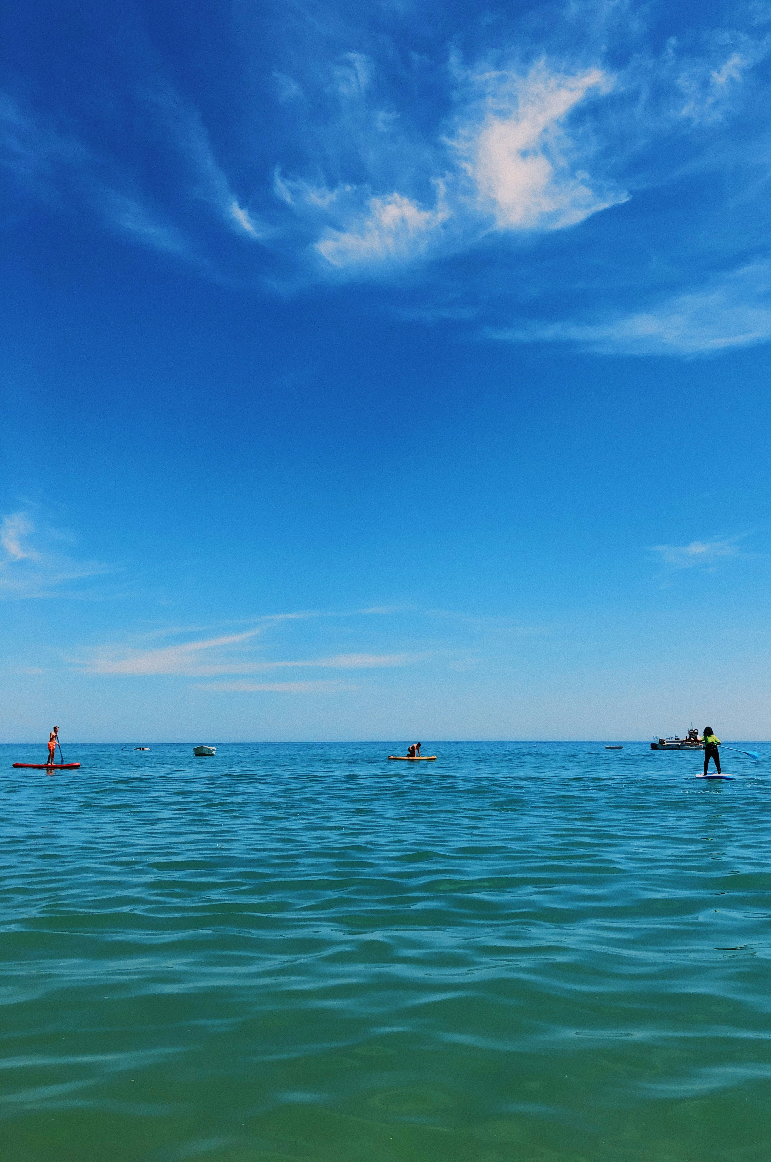 Paddleboarders gliding across calm turquoise waters under a clear blue sky with wispy clouds.