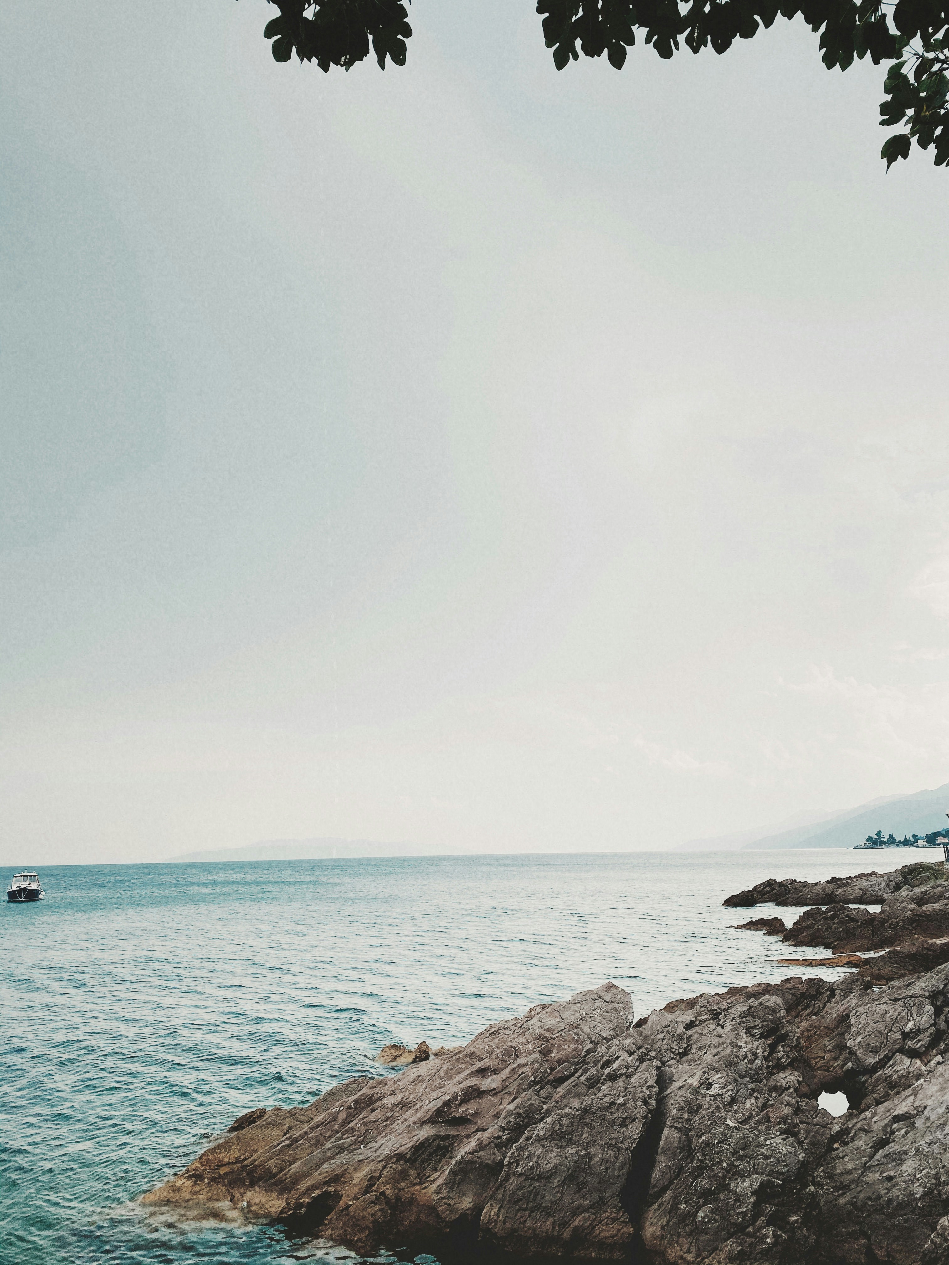 Rocky coastline with a lone boat on the serene Adriatic Sea under a pale sky.