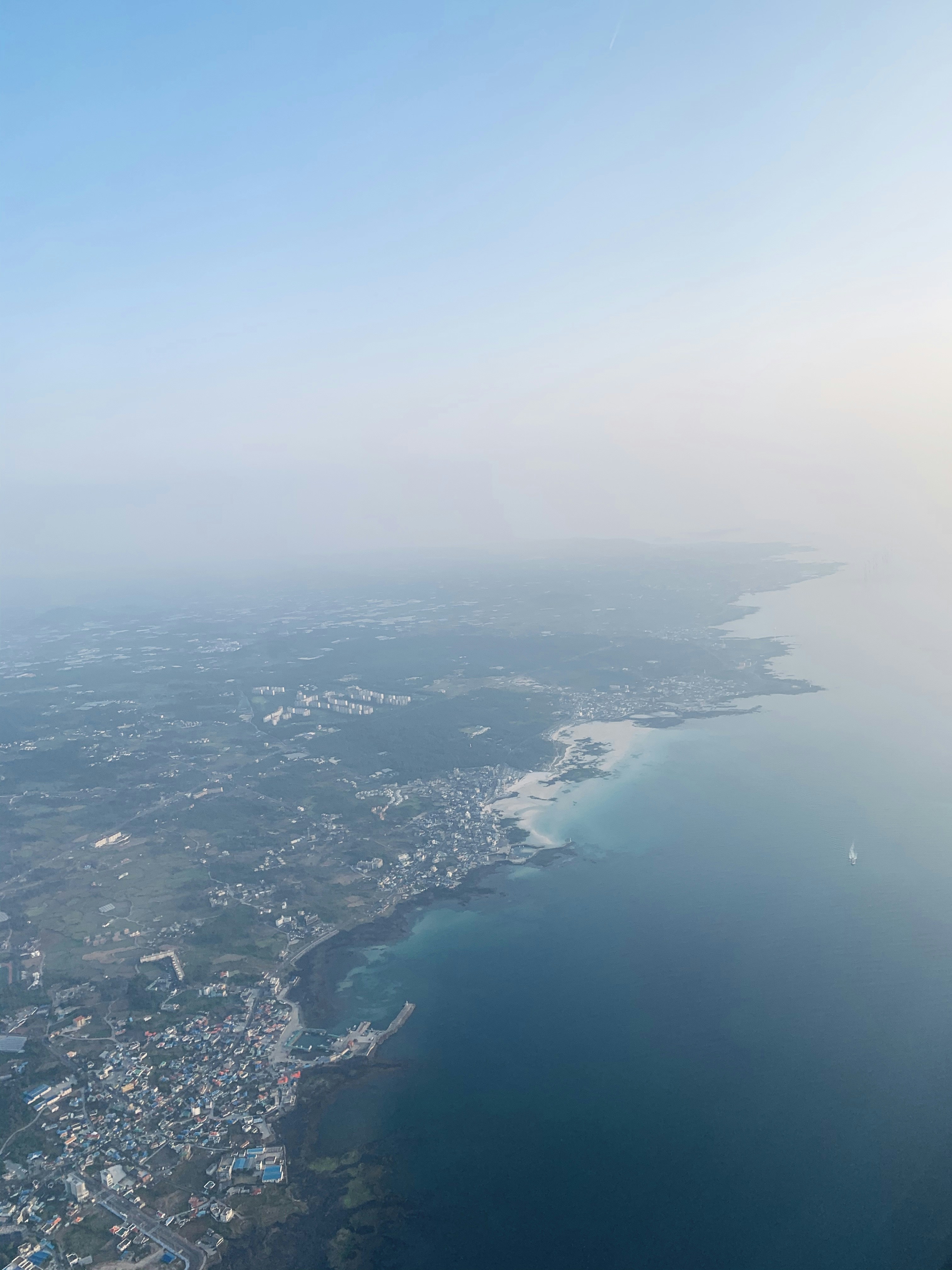 Aerial view showcasing the coastline blending with the ocean, revealing a harmonious mix of land and water. The hazy horizon adds a dreamy quality to the scene.