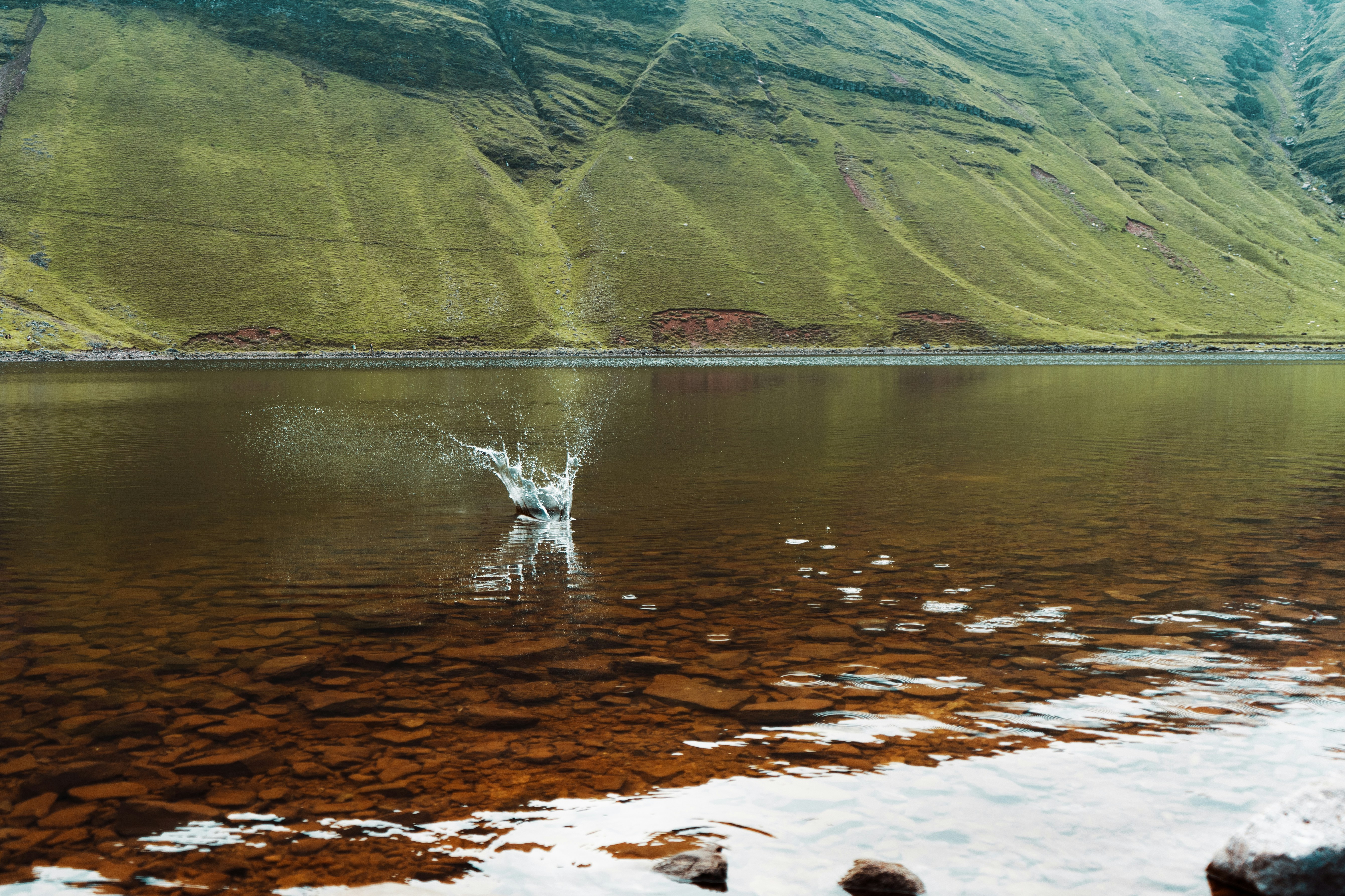 Water splashing as an object breaks the surface of a serene lake surrounded by lush green hills.