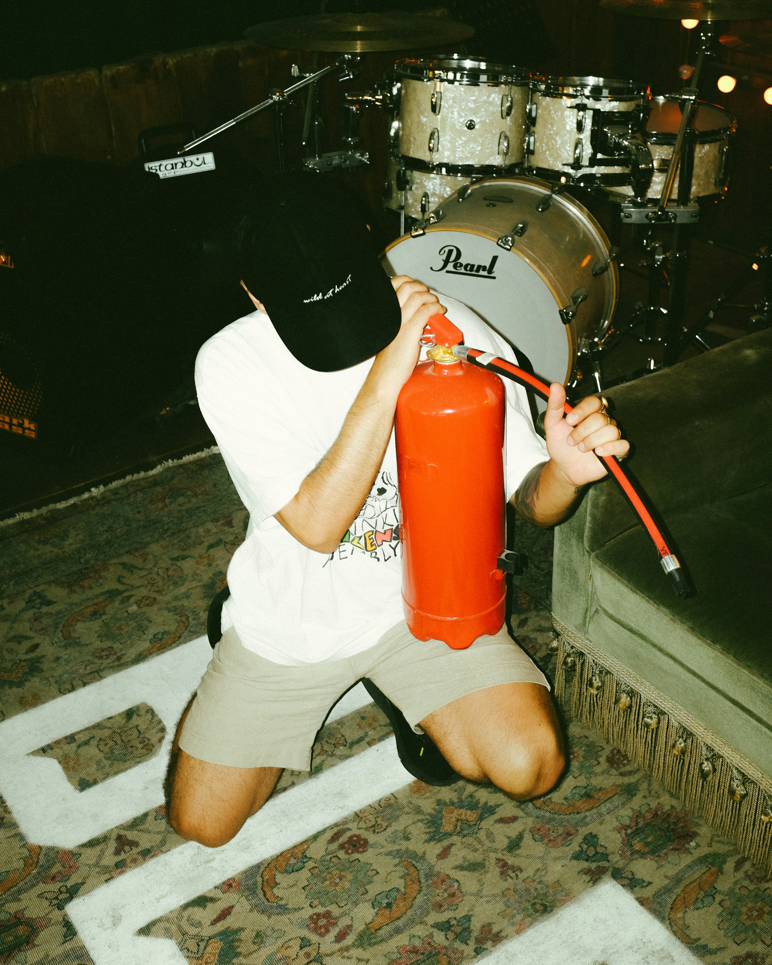 Red Extinguisher, Dim Stage: A Candid Pause Behind the Drum Kit