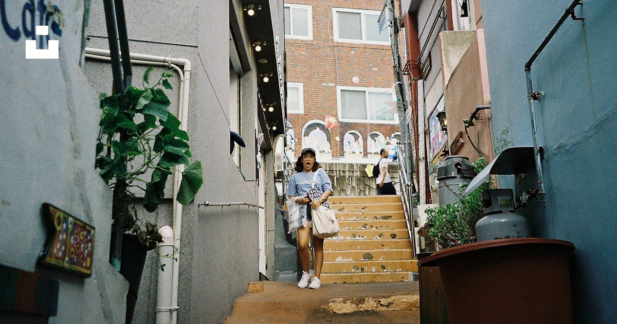 낮 동안 갈색 콘크리트 건물 옆에 서 있는 흰색 셔츠와 검은 바지를 입은 여자 사진 Unsplash의 무료 사람 이미지
