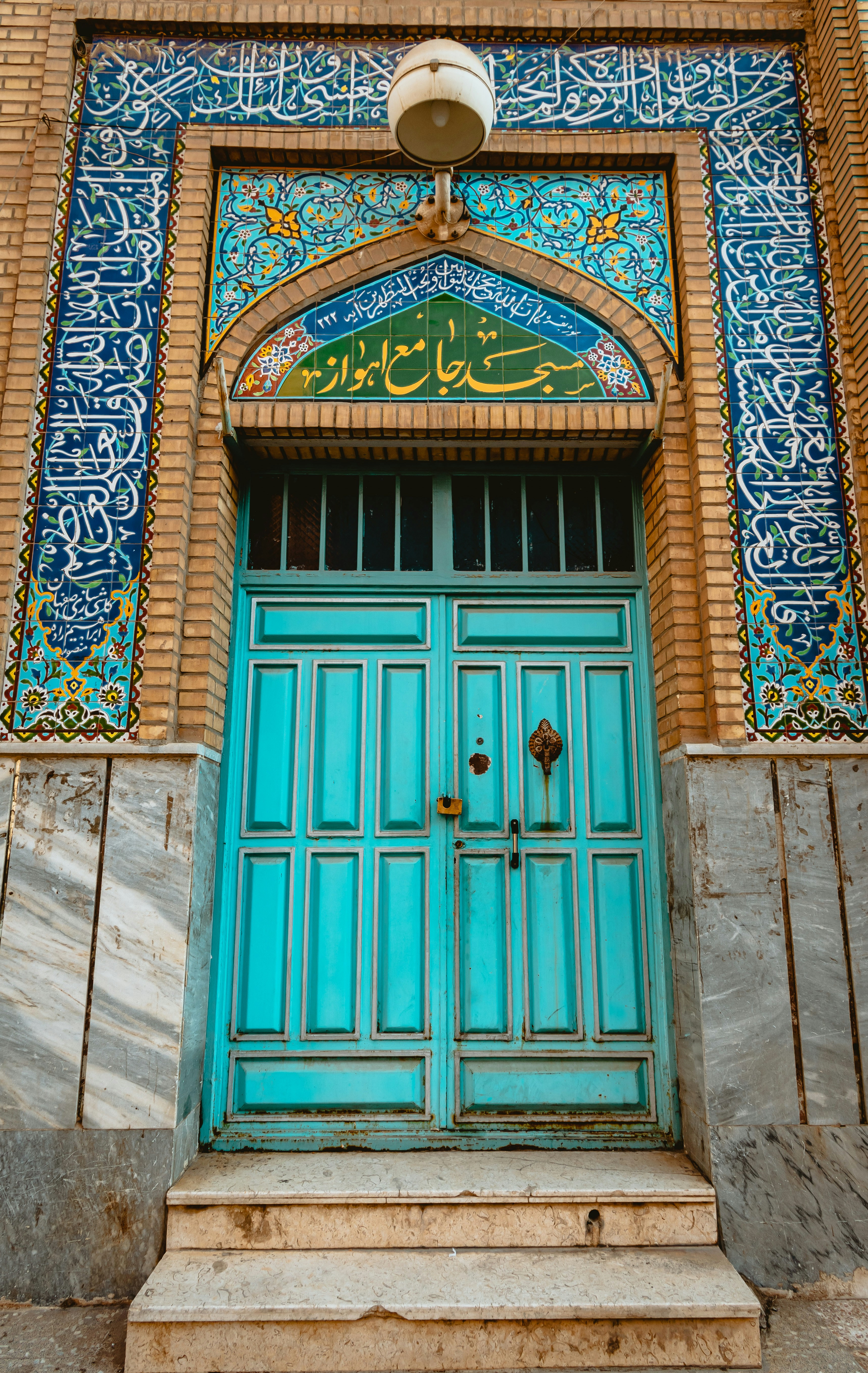 Intricately tiled doorway adorned with vibrant colors and calligraphy, showcasing traditional architectural beauty. The turquoise door serves as a striking focal point.