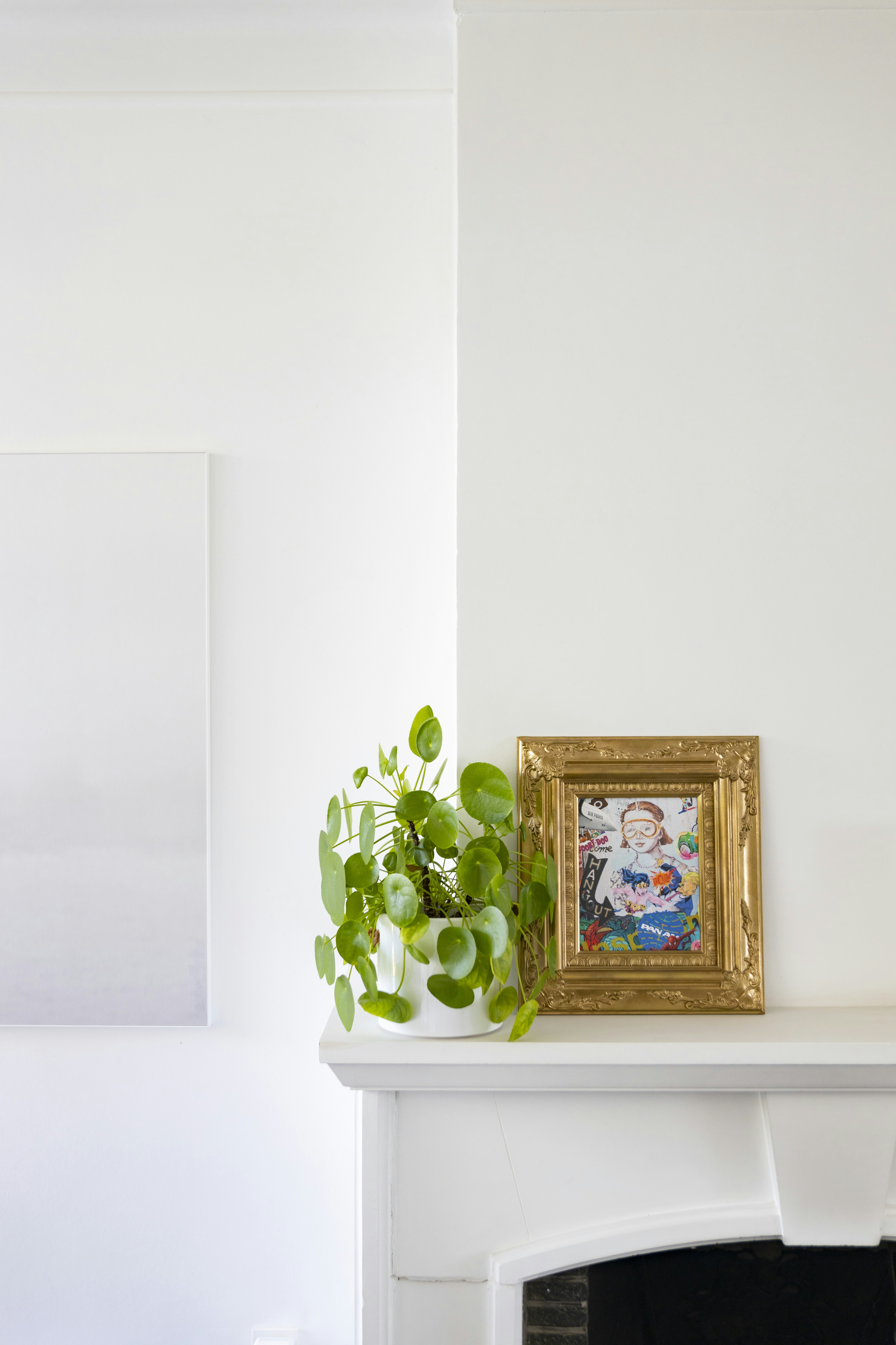 A lively potted plant sits beside a colorful framed artwork on a white mantel, showcasing a blend of nature and creativity in a minimalist setting.