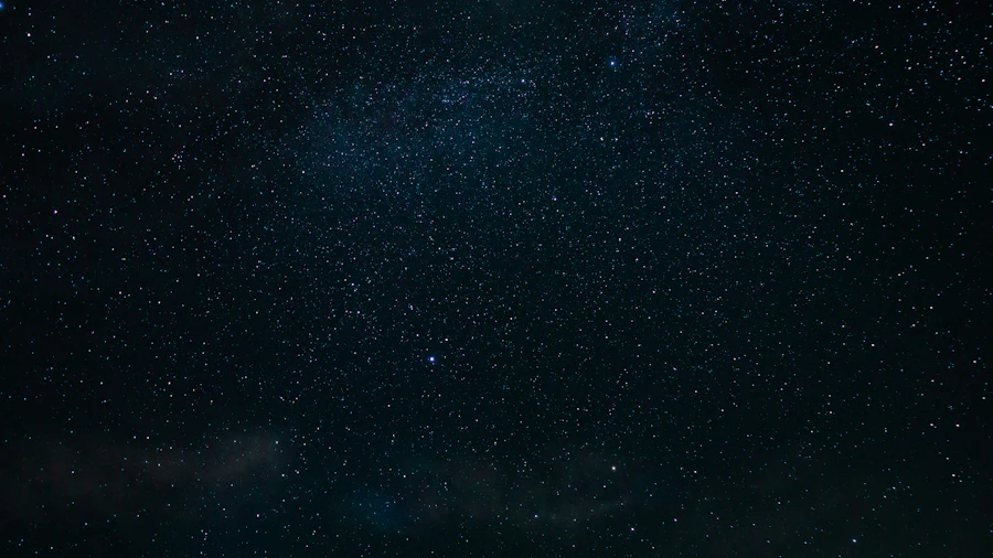 Dense field of stars scattered across a dark night sky with faint wisps of nebula-like cloud. A few brighter stars stand out near the center.