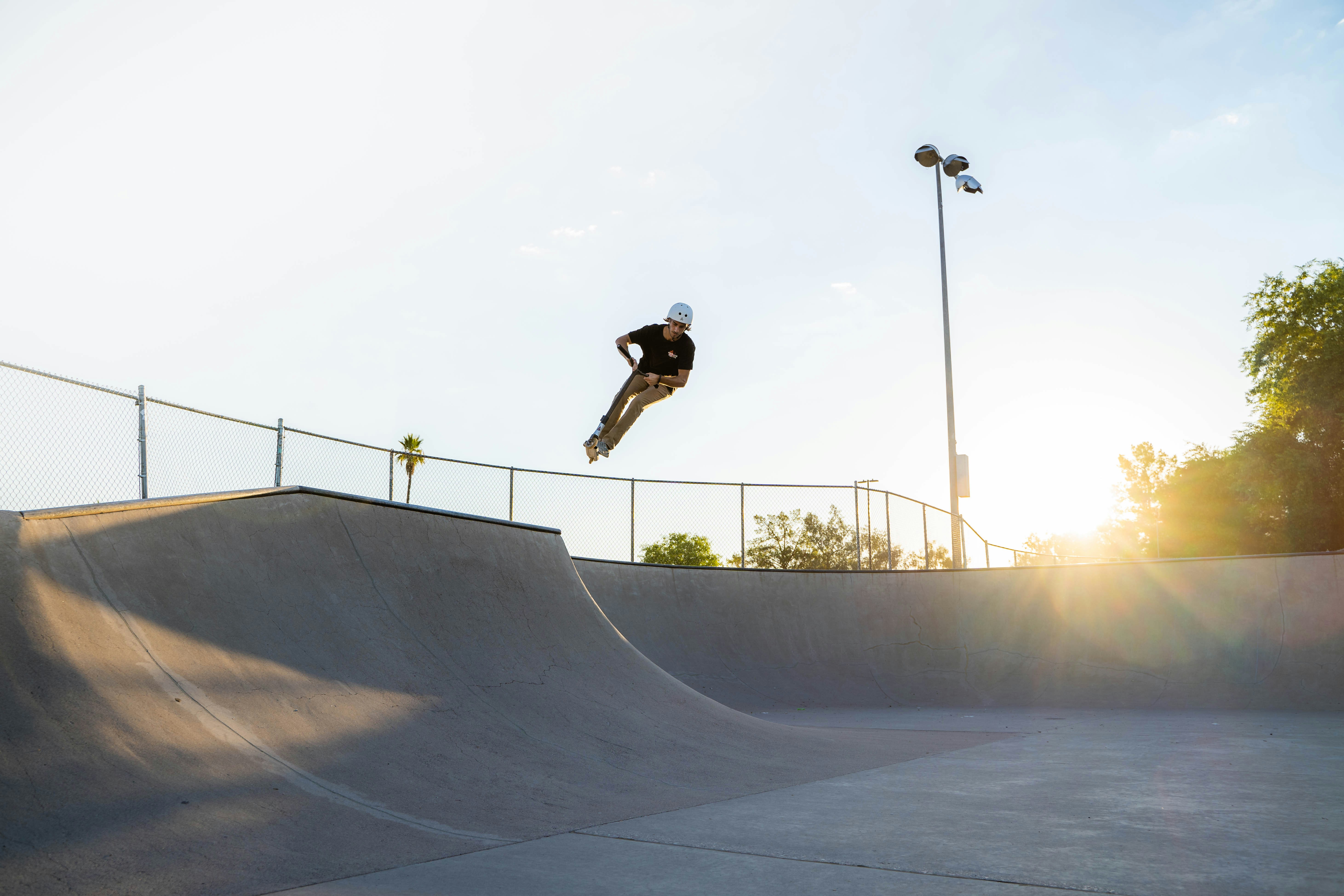 Skateboarder performing a mid-air trick above a skate park ramp during sunset.
