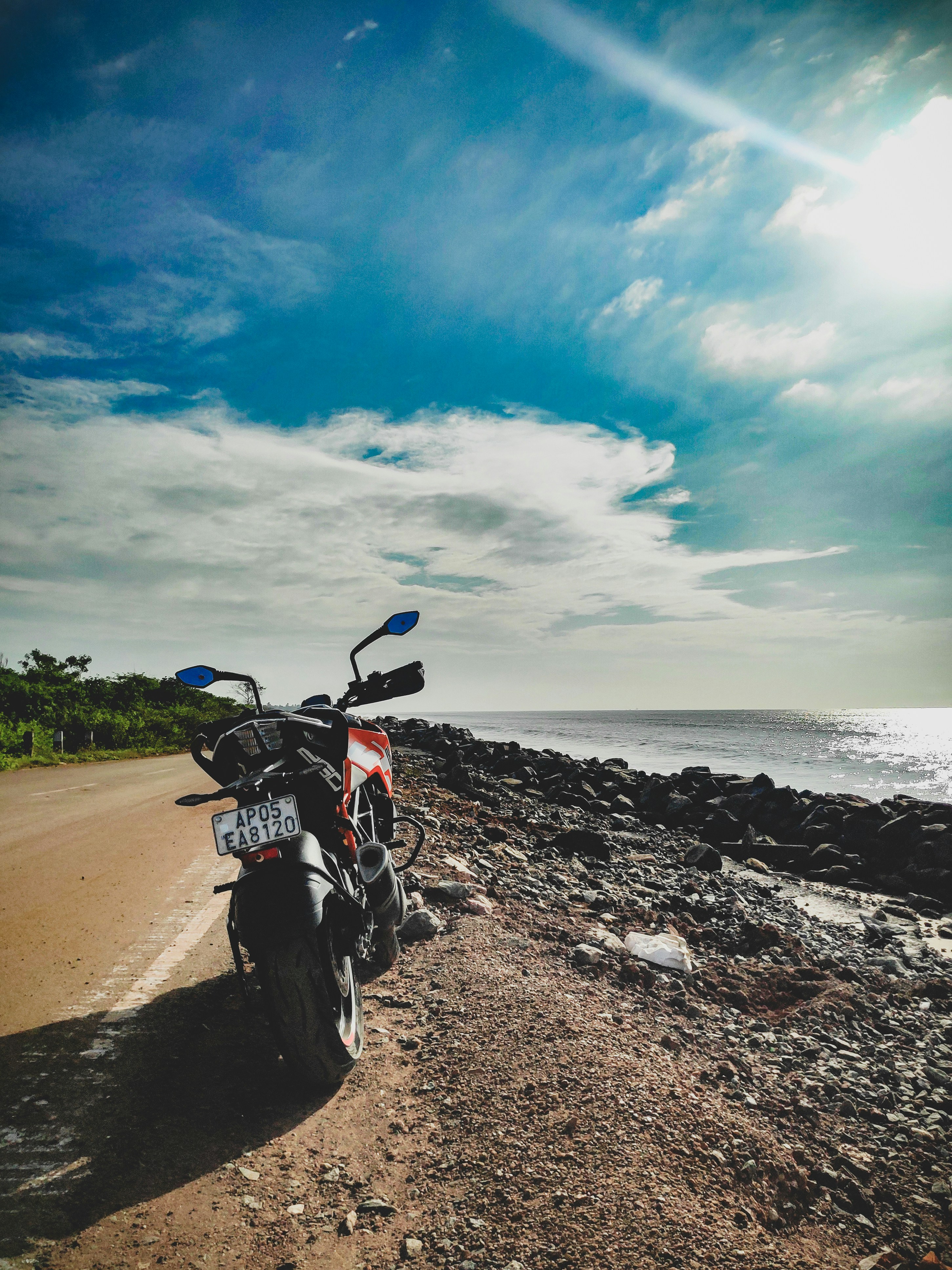 Motorcycle parked on a rocky shoreline under a vibrant sky, with waves gently lapping at the coast.