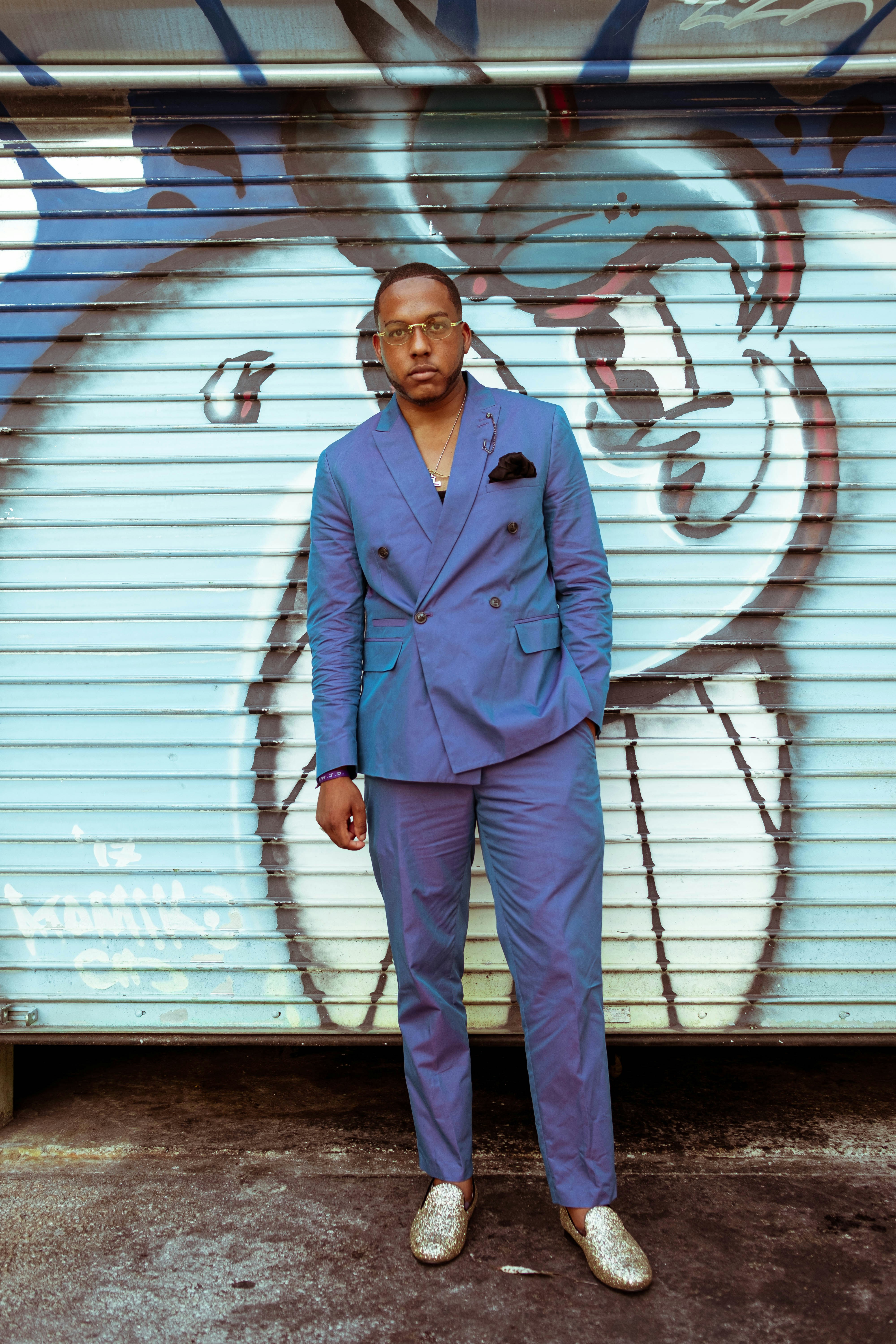 A stylish individual in a tailored blue suit stands confidently in front of a vibrant graffiti backdrop, showcasing a blend of urban art and contemporary fashion.