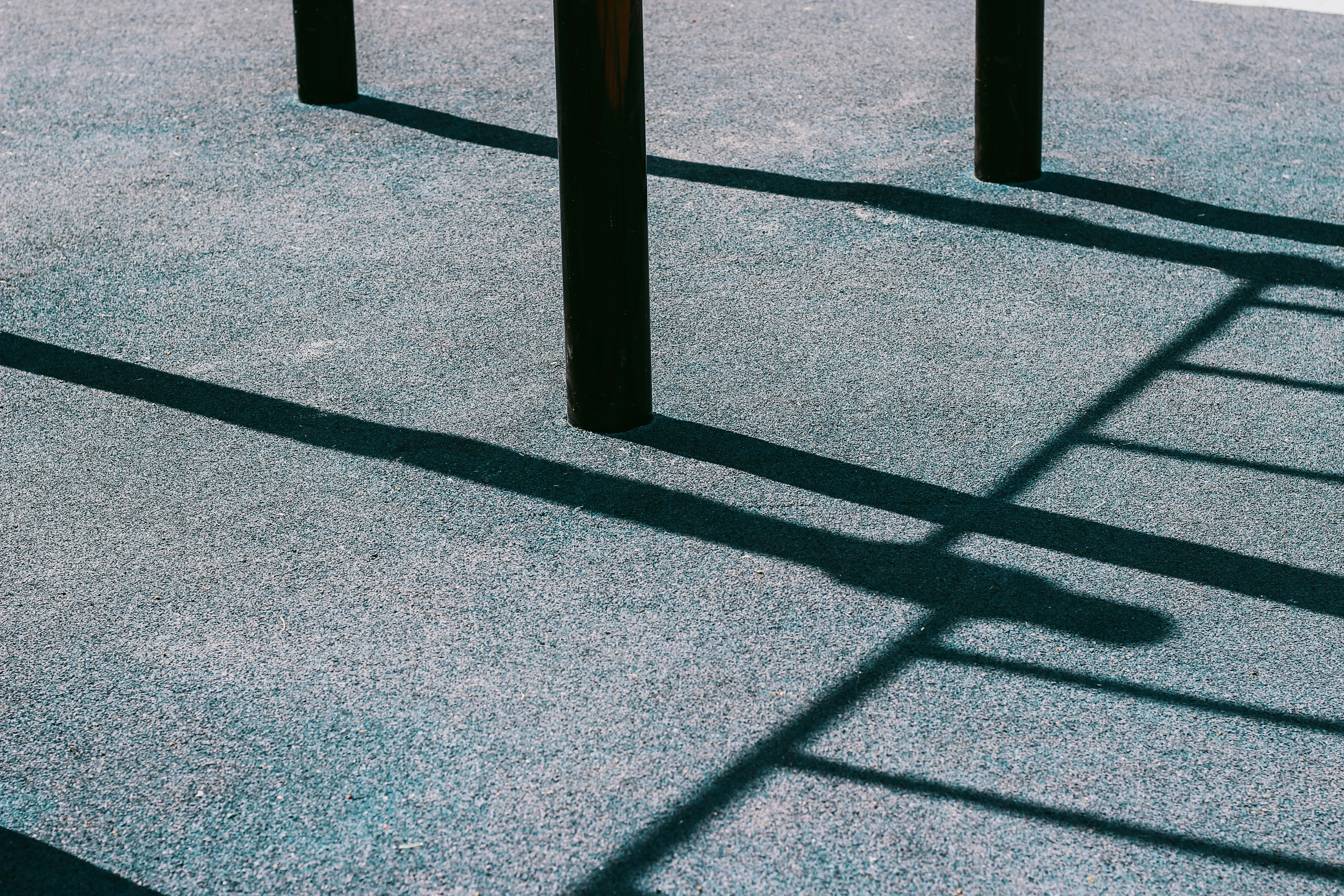 Playground equipment casting intricate shadows on rubberized flooring, emphasizing texture and light interplay.