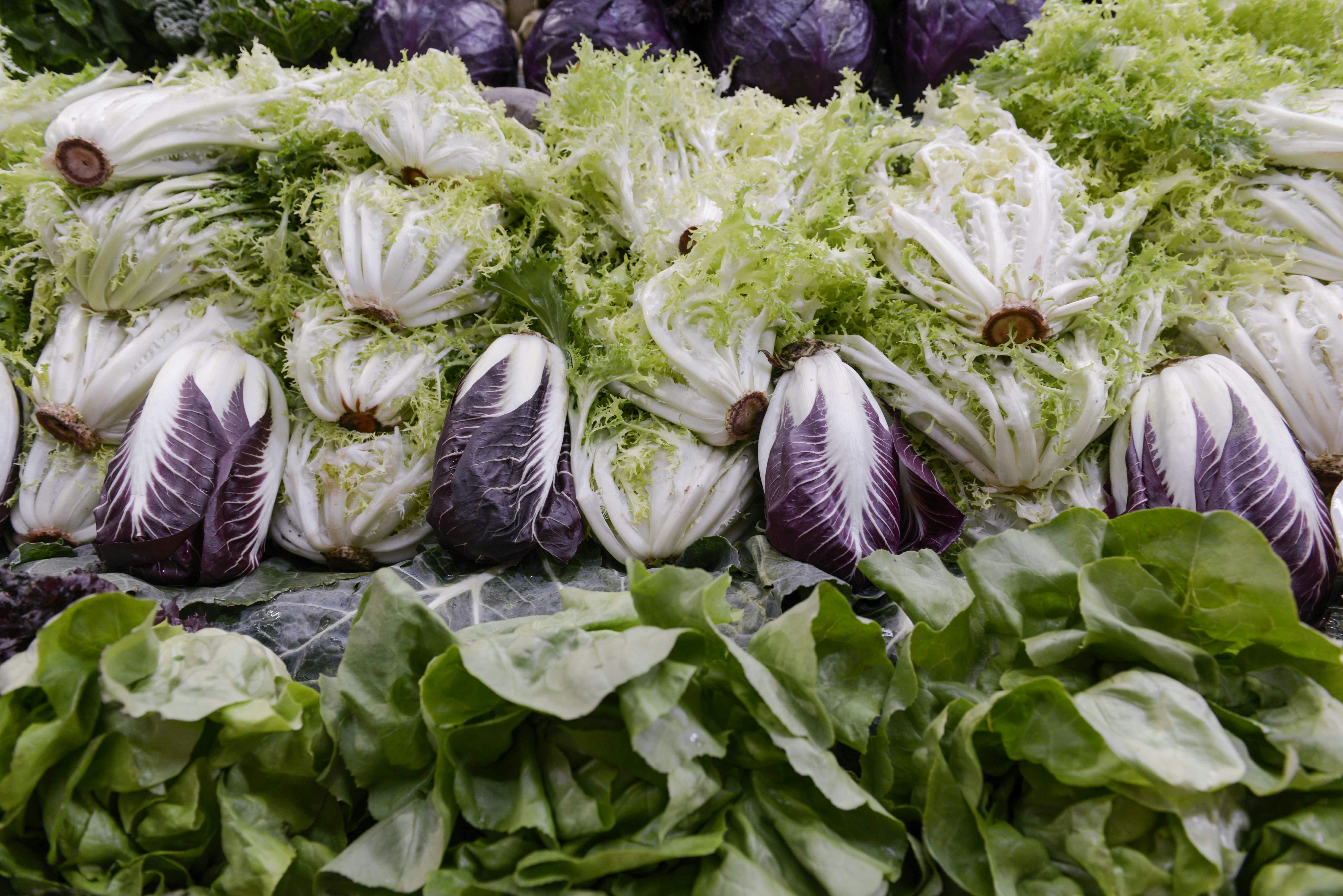 Rows of fresh leafy greens and purple cabbages arranged neatly at a market stall.