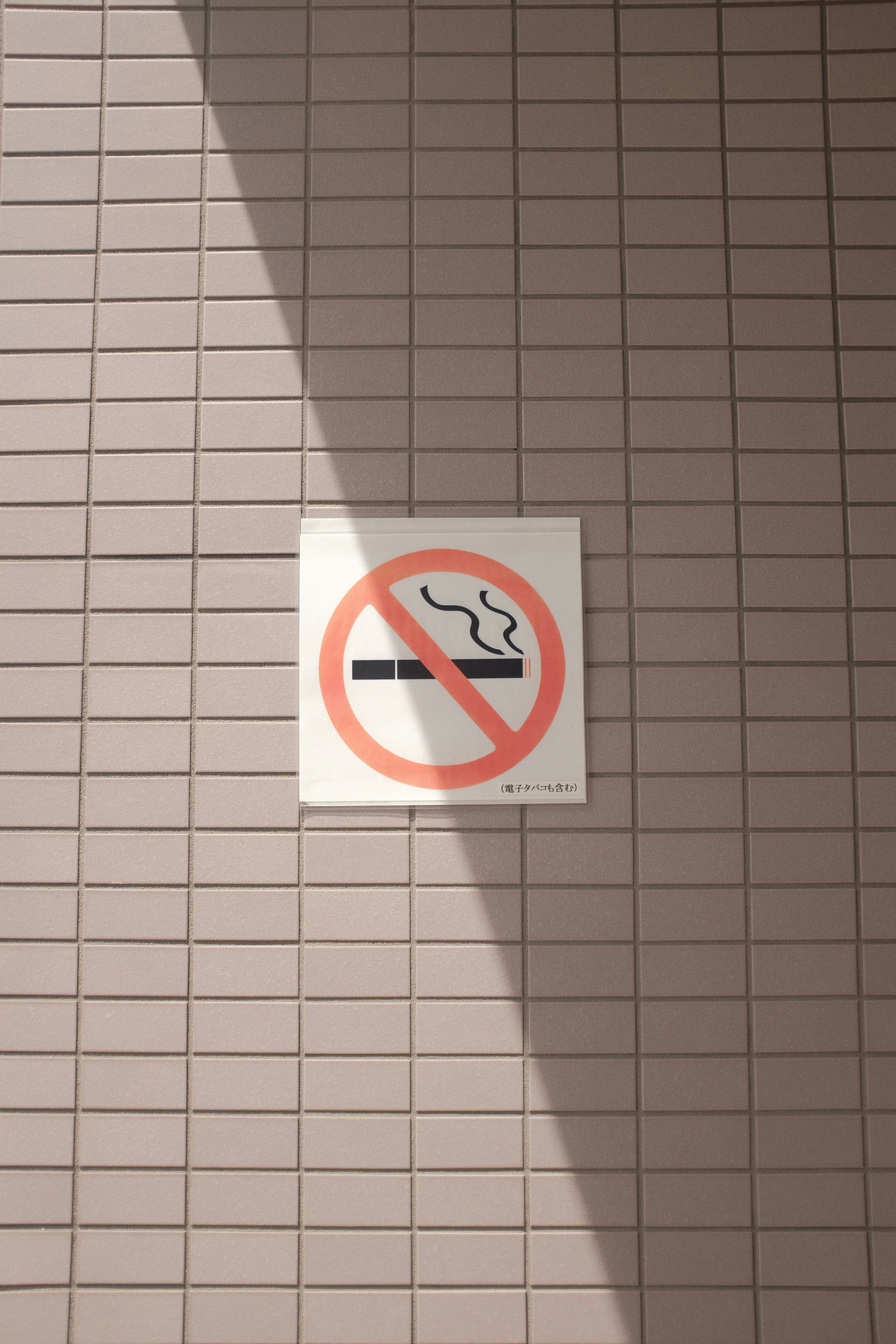 No-Smoking Sign Under a Diagonal Shadow on a Tiled Wall