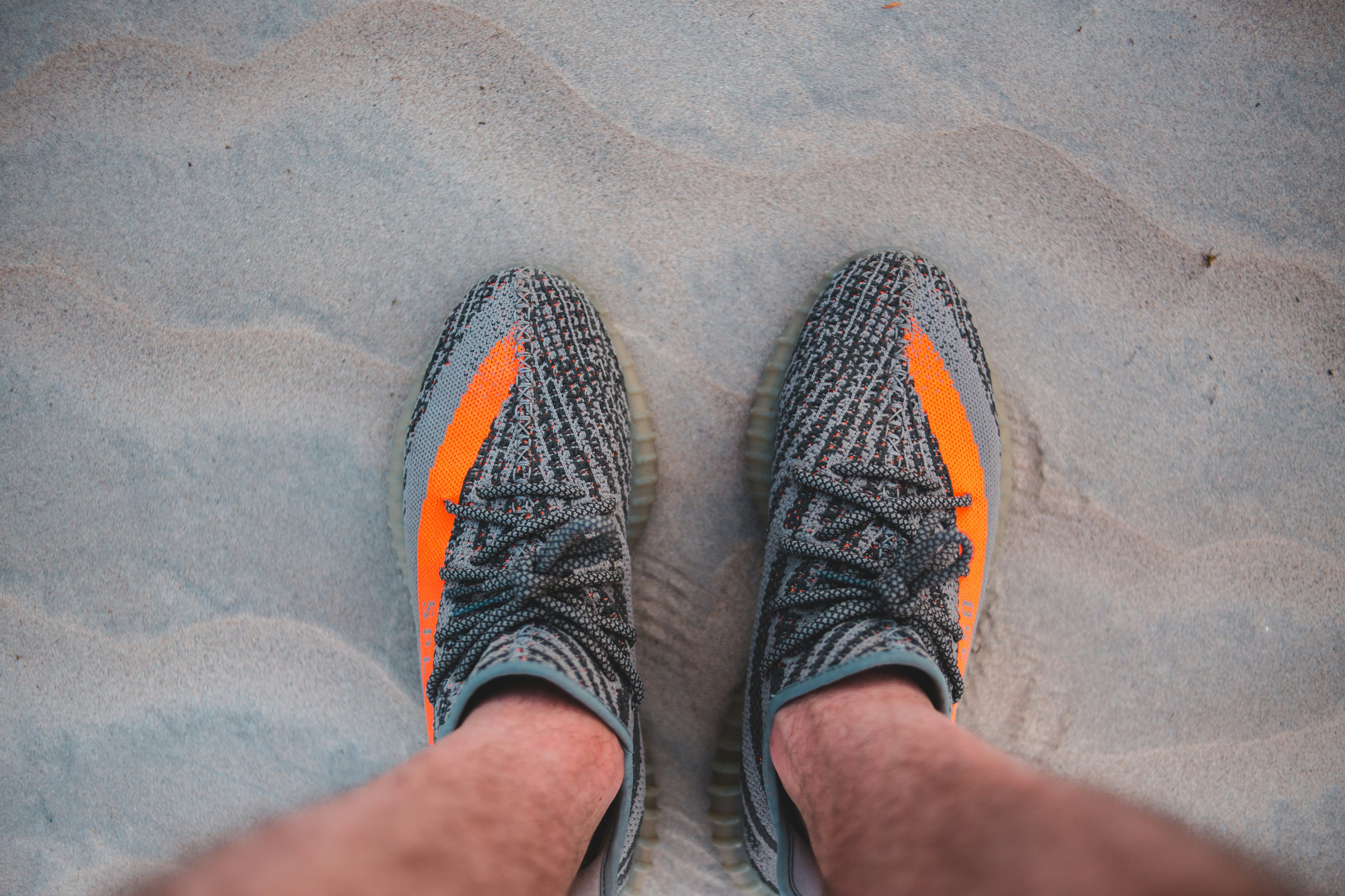 Close-up of stylish sneakers resting on sandy terrain, showcasing intricate patterns and vibrant colors. The scene captures a moment of leisure and exploration.