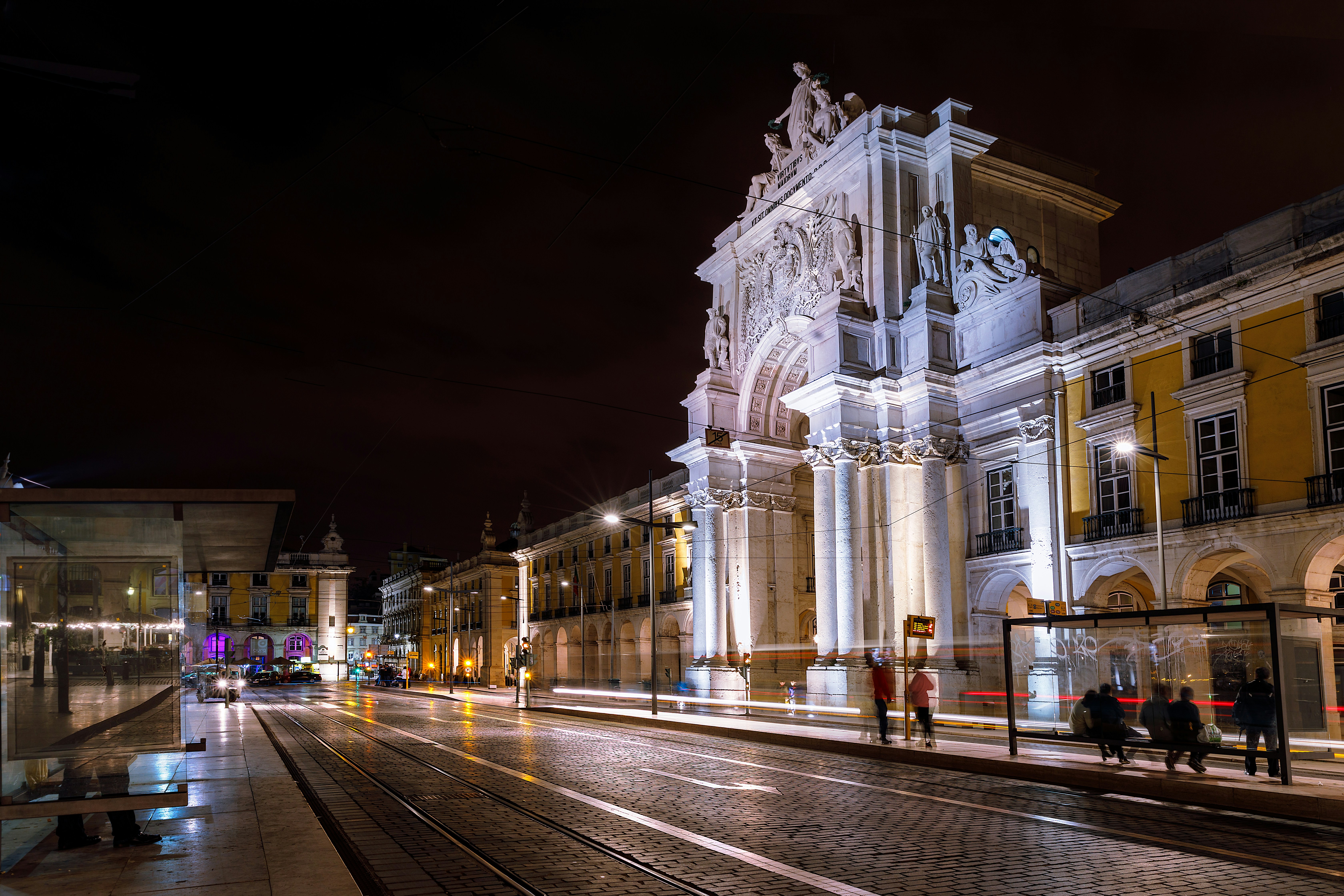 Illuminated historical archway stands prominently against a night sky, with blurred figures and light trails adding a dynamic urban feel.