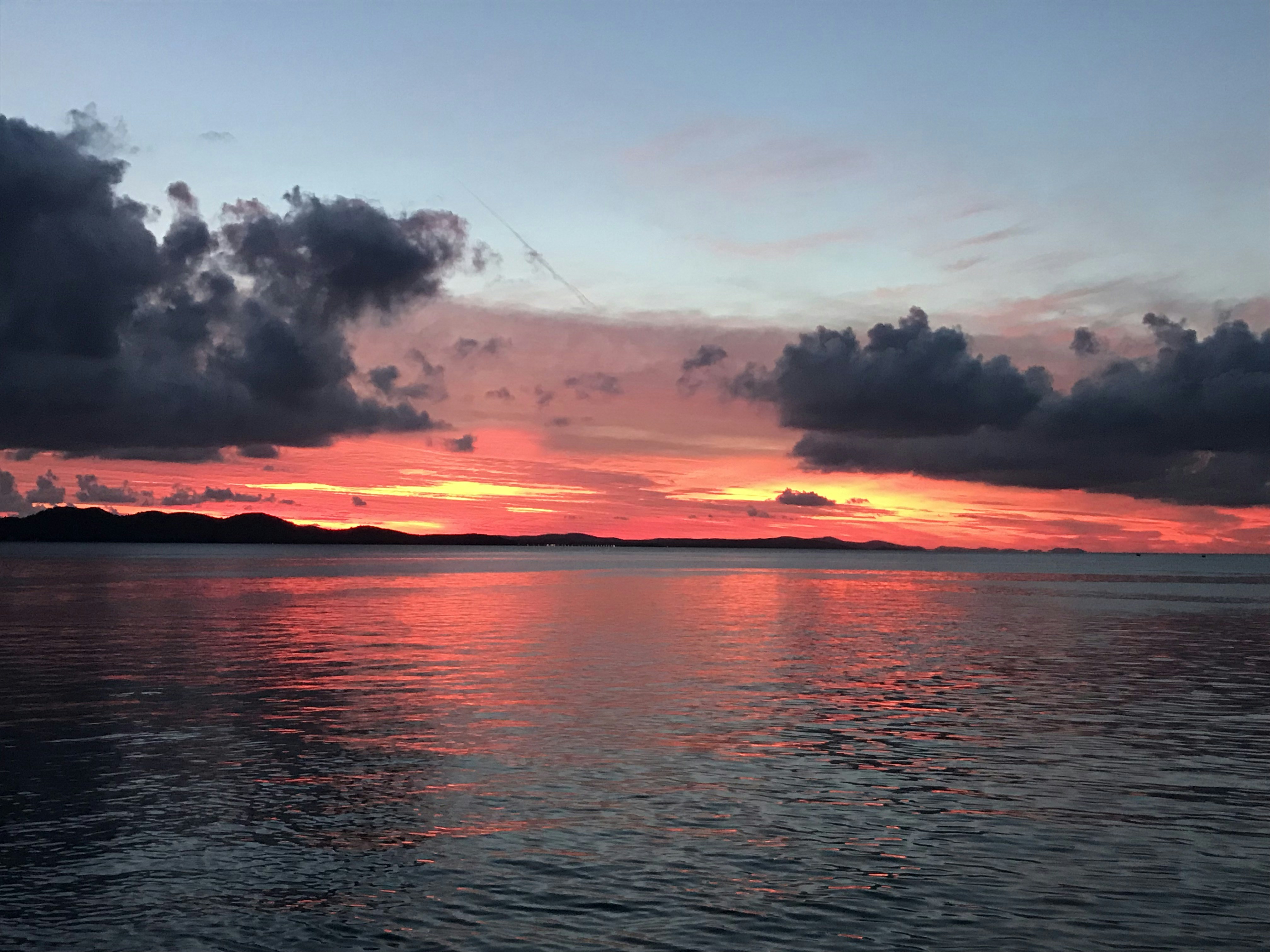 Dramatic sunset over a calm sea with silhouetted clouds and distant land.