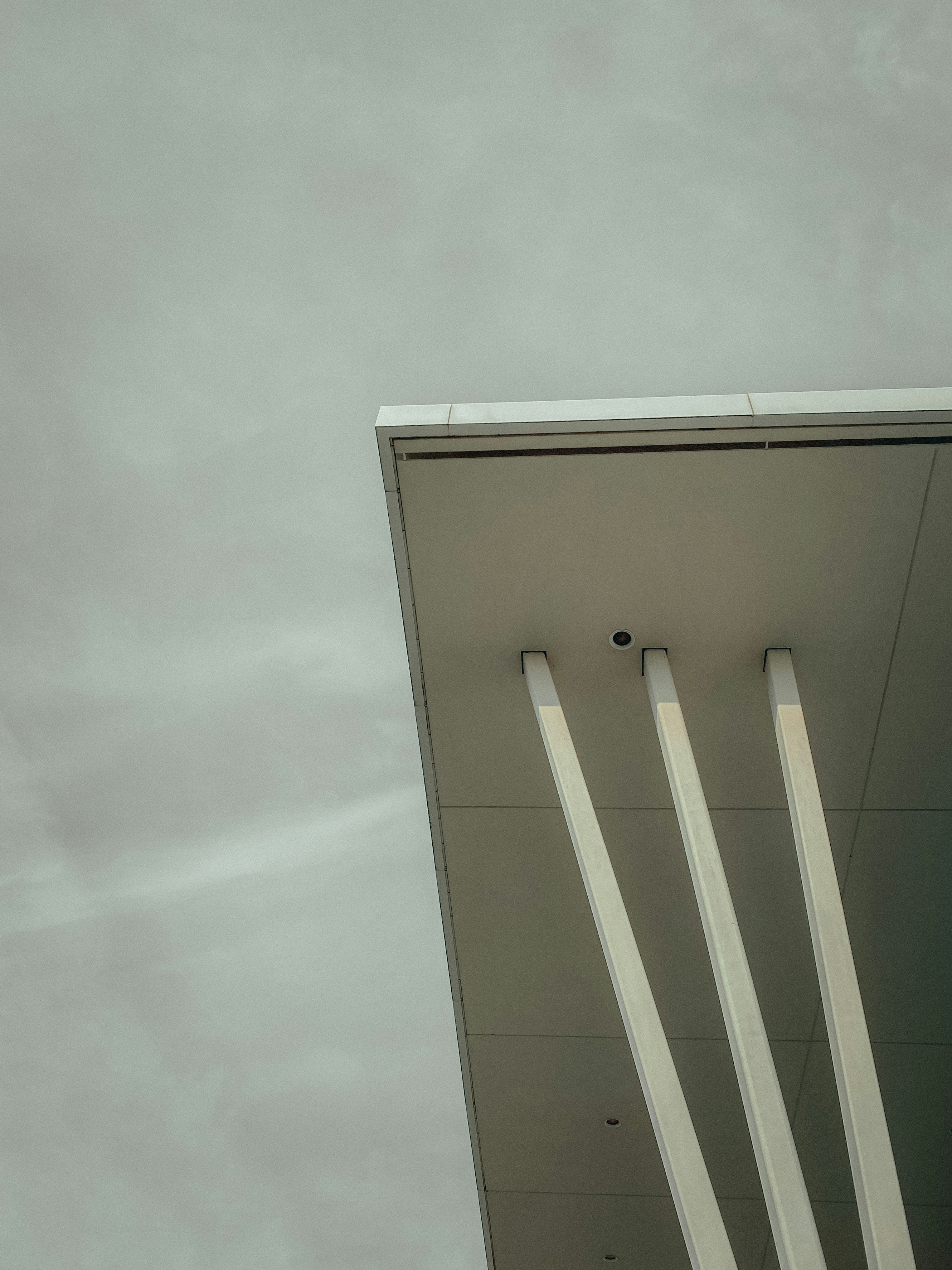 Minimalist architectural overhang featuring sleek lines and a subtle camera embedded in the structure. The cloudy sky adds depth to the composition.