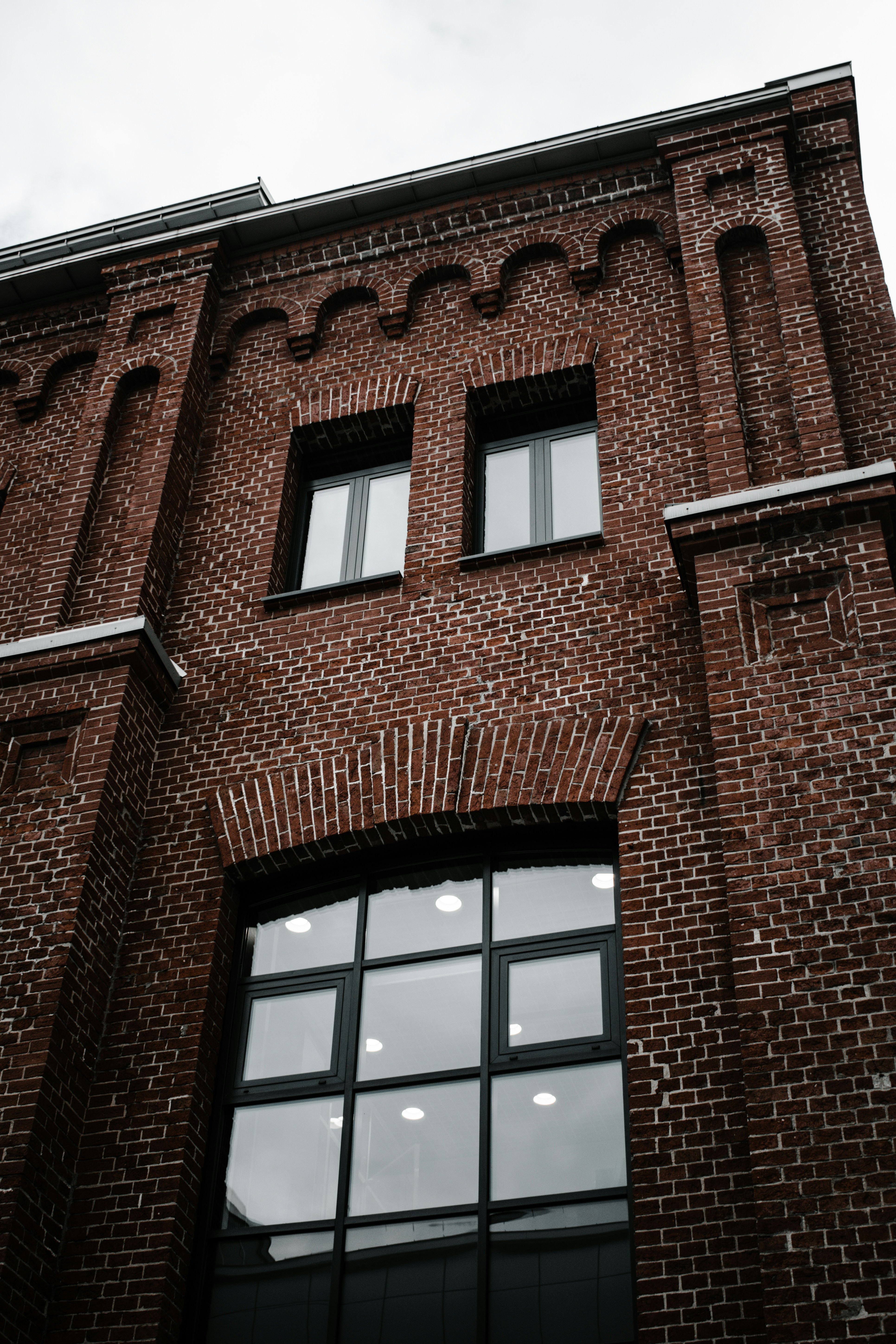 Detailed view of a brick building's facade showcasing intricate architectural elements and large windows. The structure reflects a blend of historical and modern design.