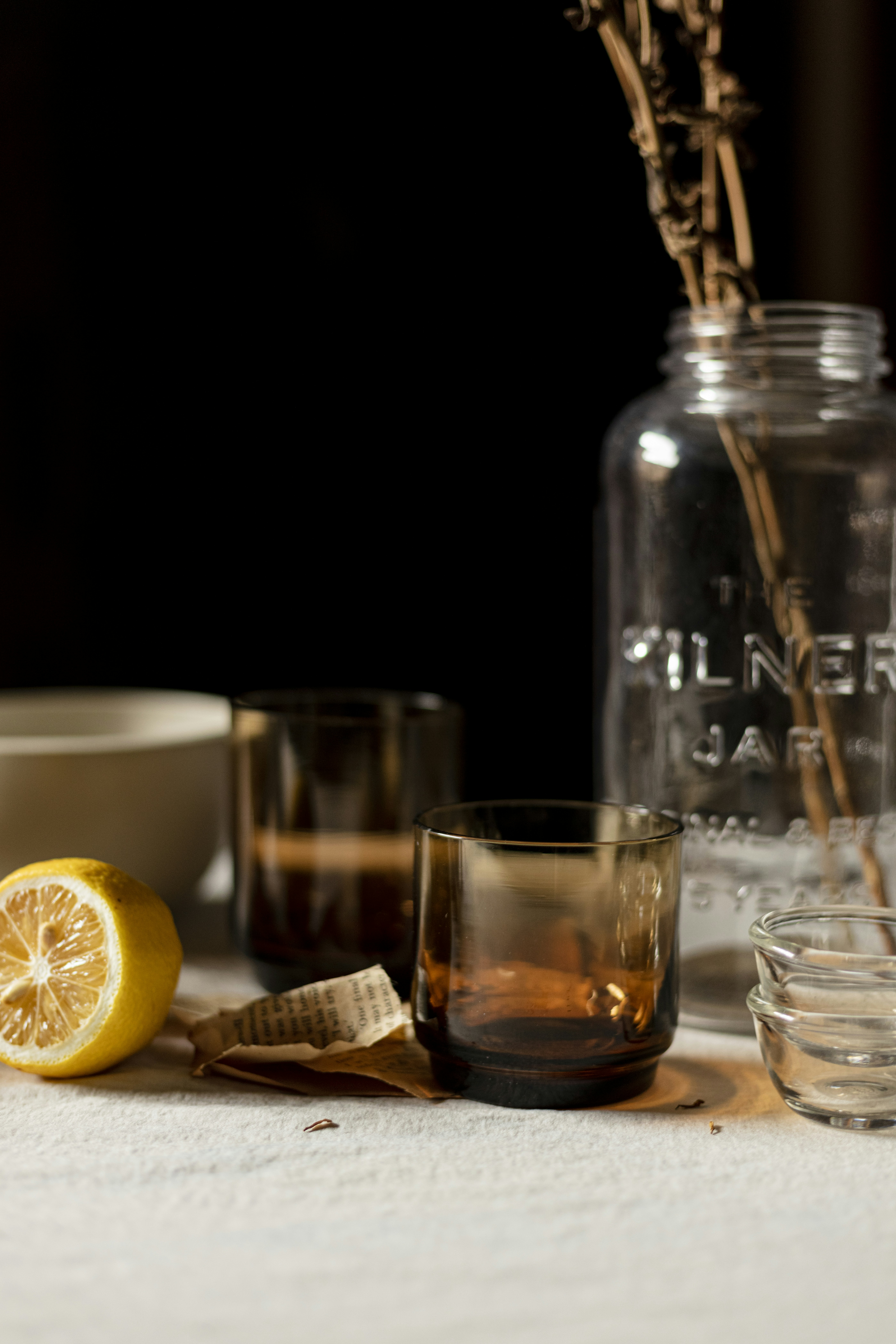 Arrangement of amber glassware, a lemon half, and a vintage jar on a softly lit table. The composition emphasizes textures and subtle colors.