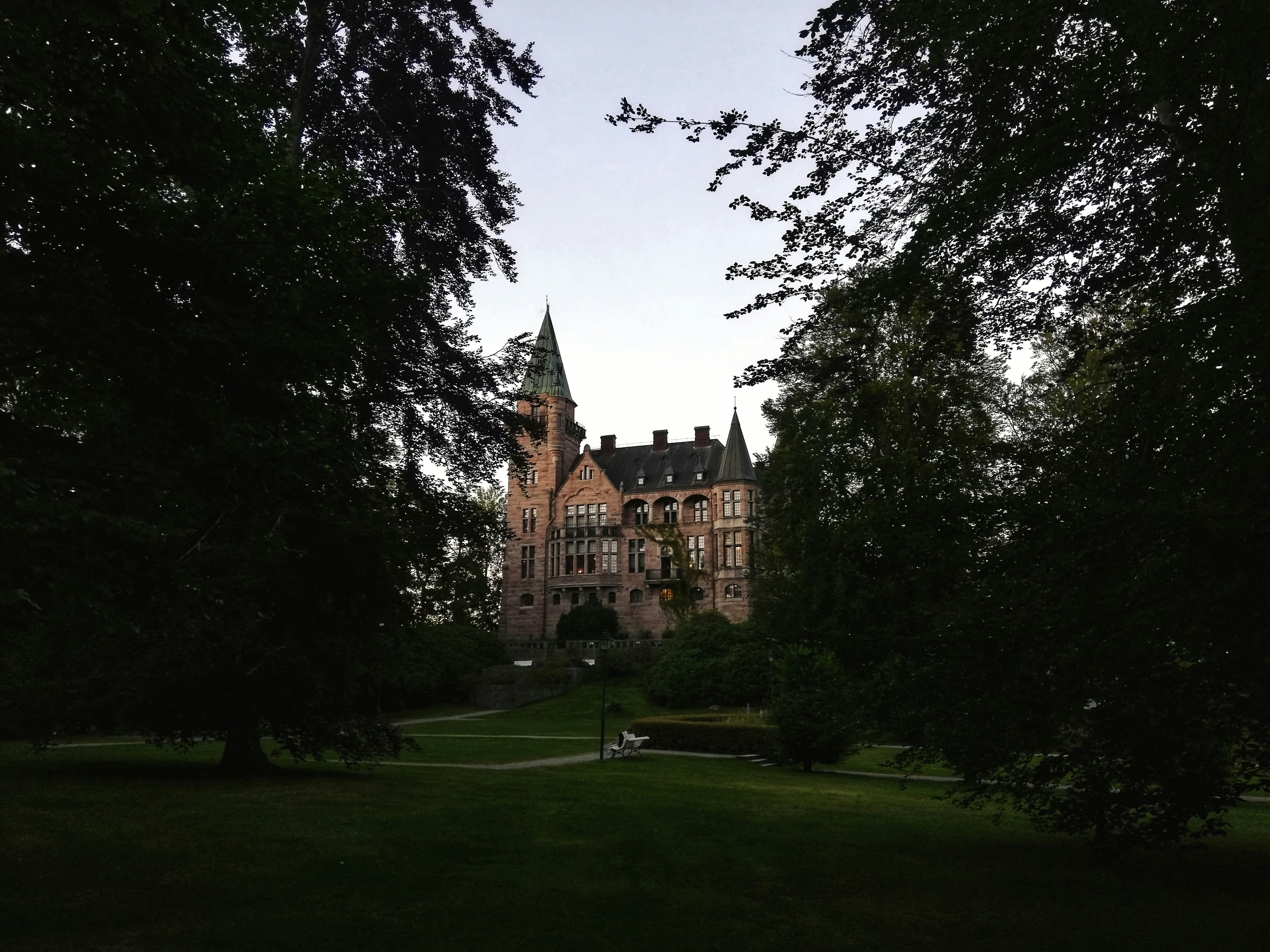 Historic manor nestled among lush greenery, showcasing intricate architecture against a twilight sky.