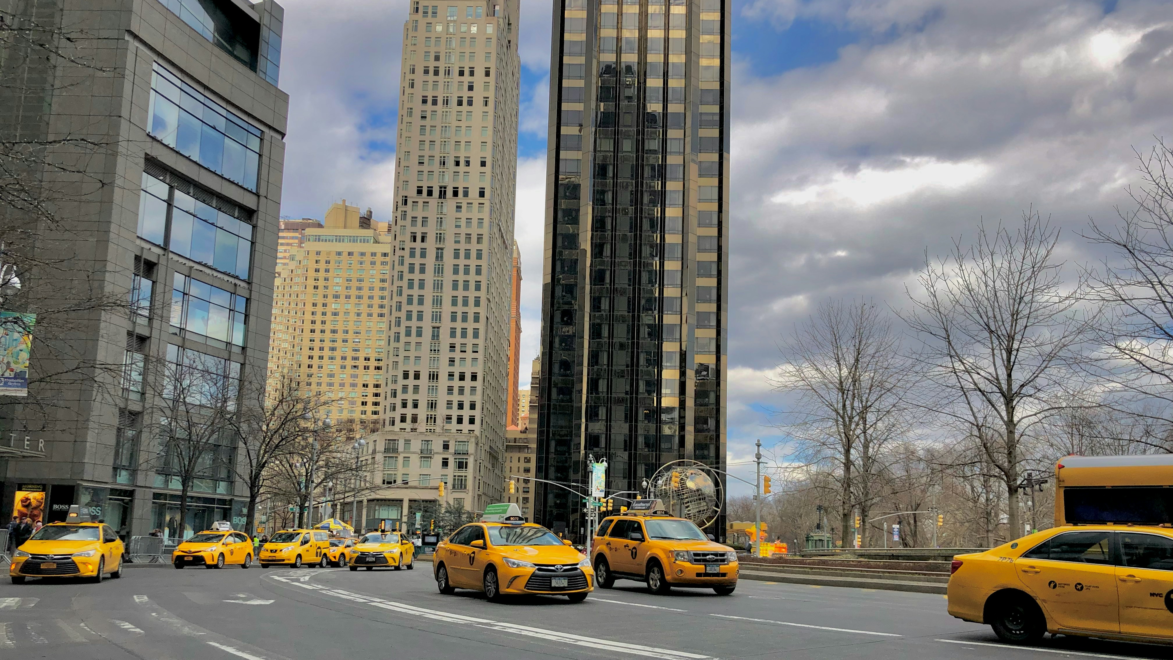 Yellow taxis navigate a bustling cityscape framed by towering skyscrapers under a partly cloudy sky.
