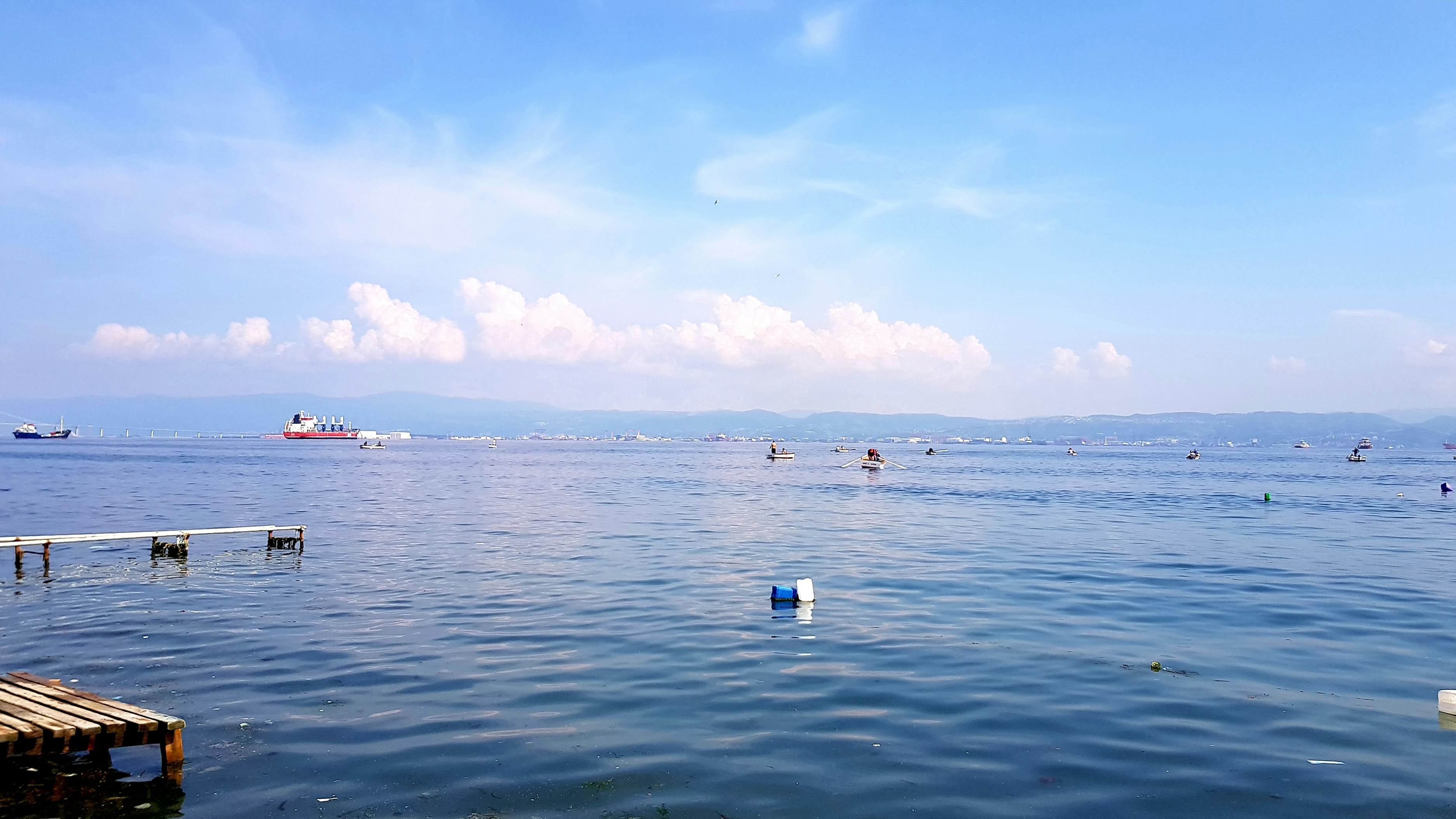Calm sea with a few paddleboarders and a distant ship under a clear, blue sky.