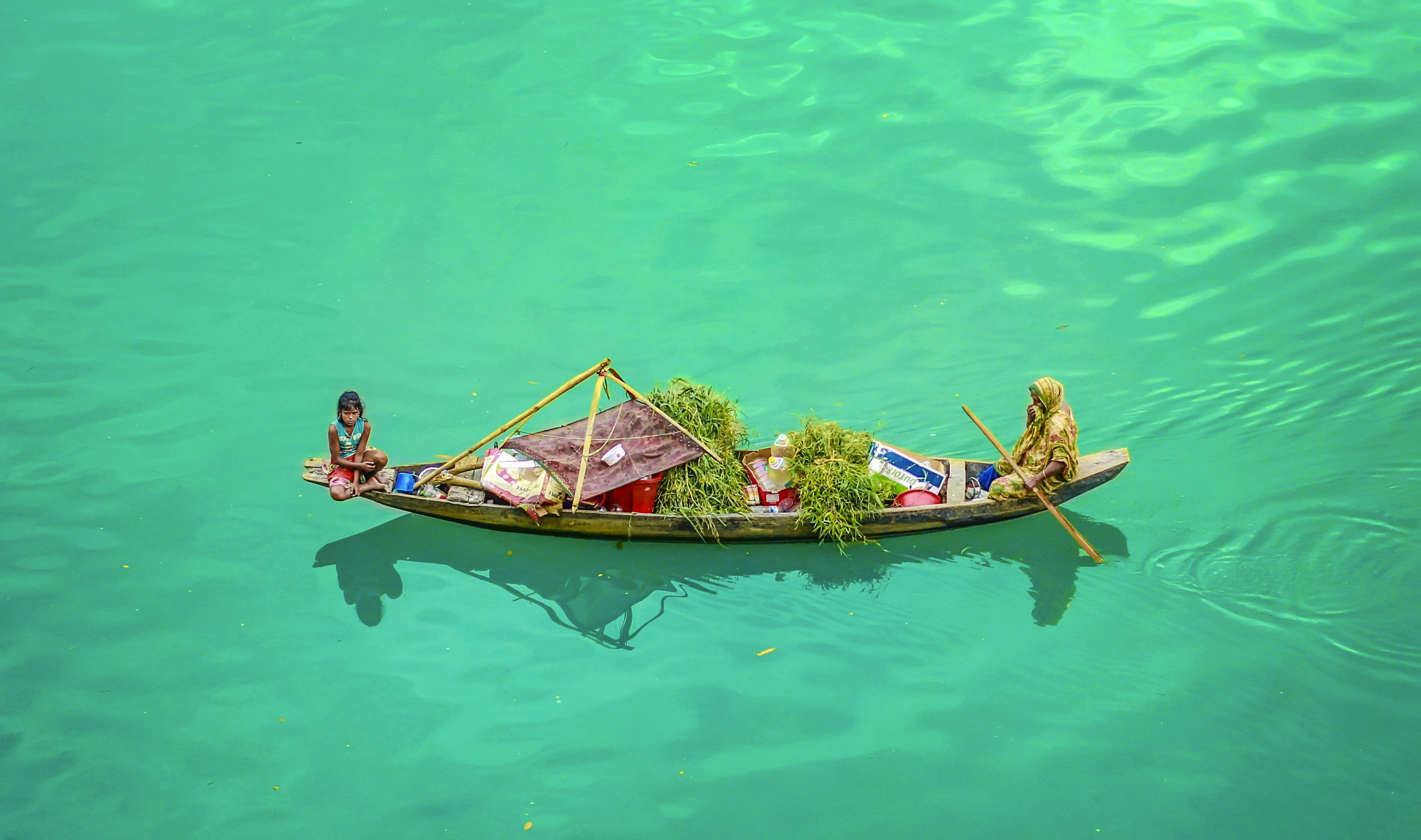 Turquoise Wake: A Simple Long-Tail Boat Carries Green Harvest on Cerulean Seas
