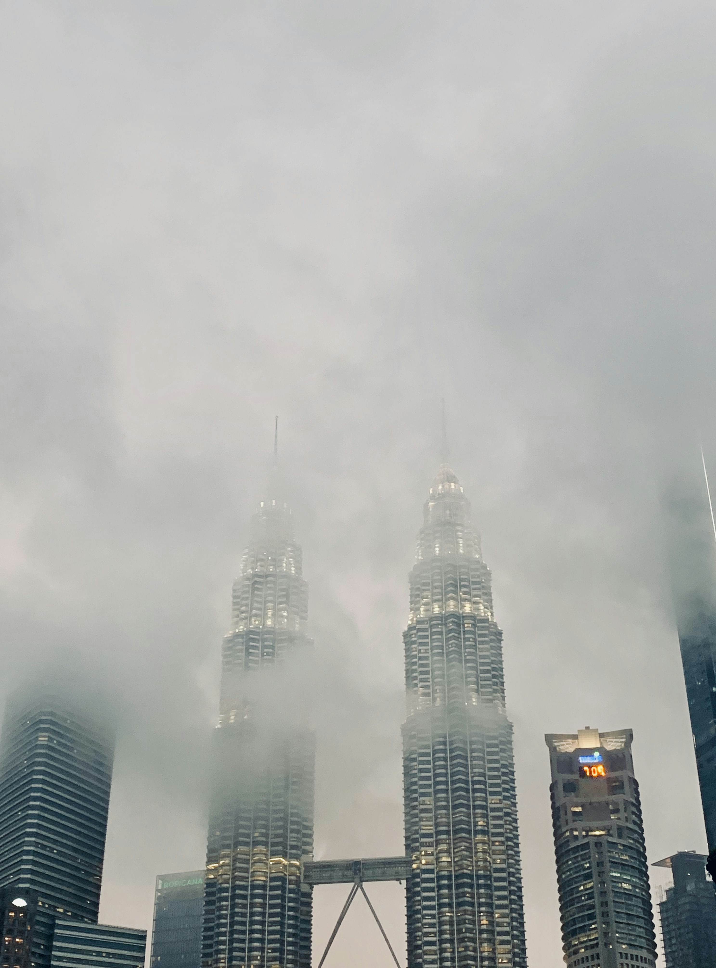 Petronas Towers partially shrouded in mist, rising above the urban skyline, creating an ethereal atmosphere.