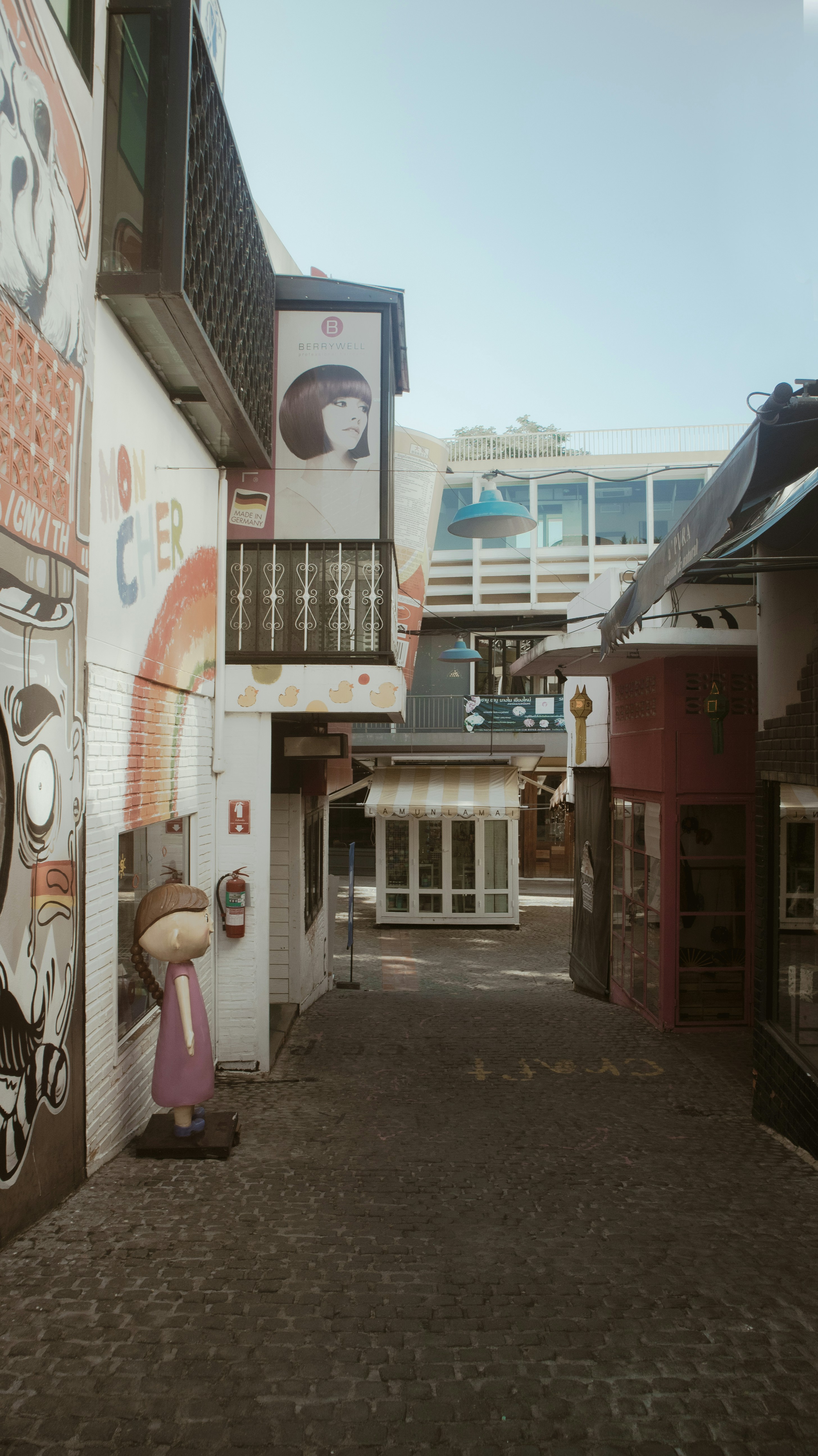 Colorful murals and a quirky sculpture create a vibrant atmosphere in a narrow alleyway lined with shops. The scene invites exploration and creativity.