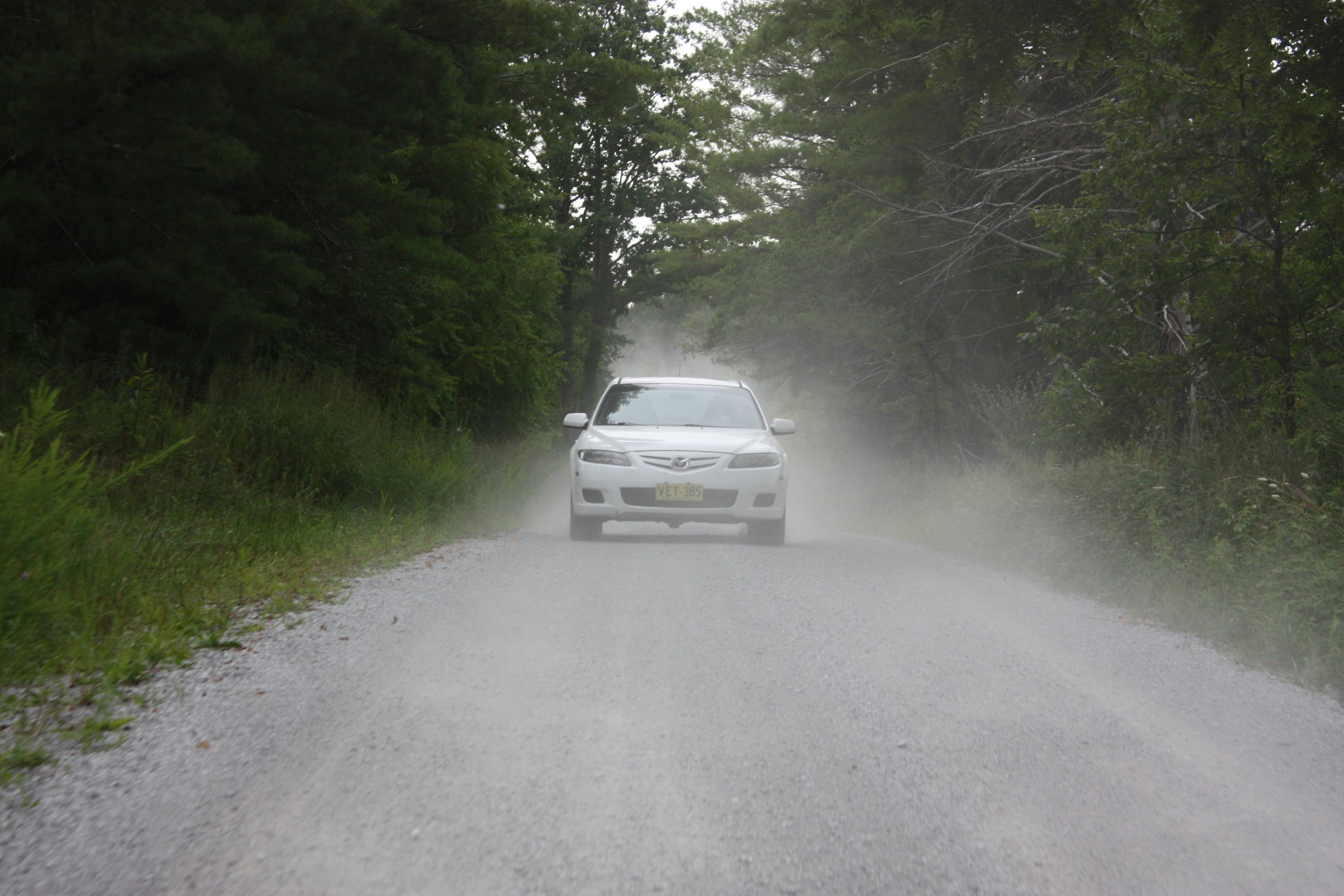Dusty Approach: White sedan carving through a forest gravel road