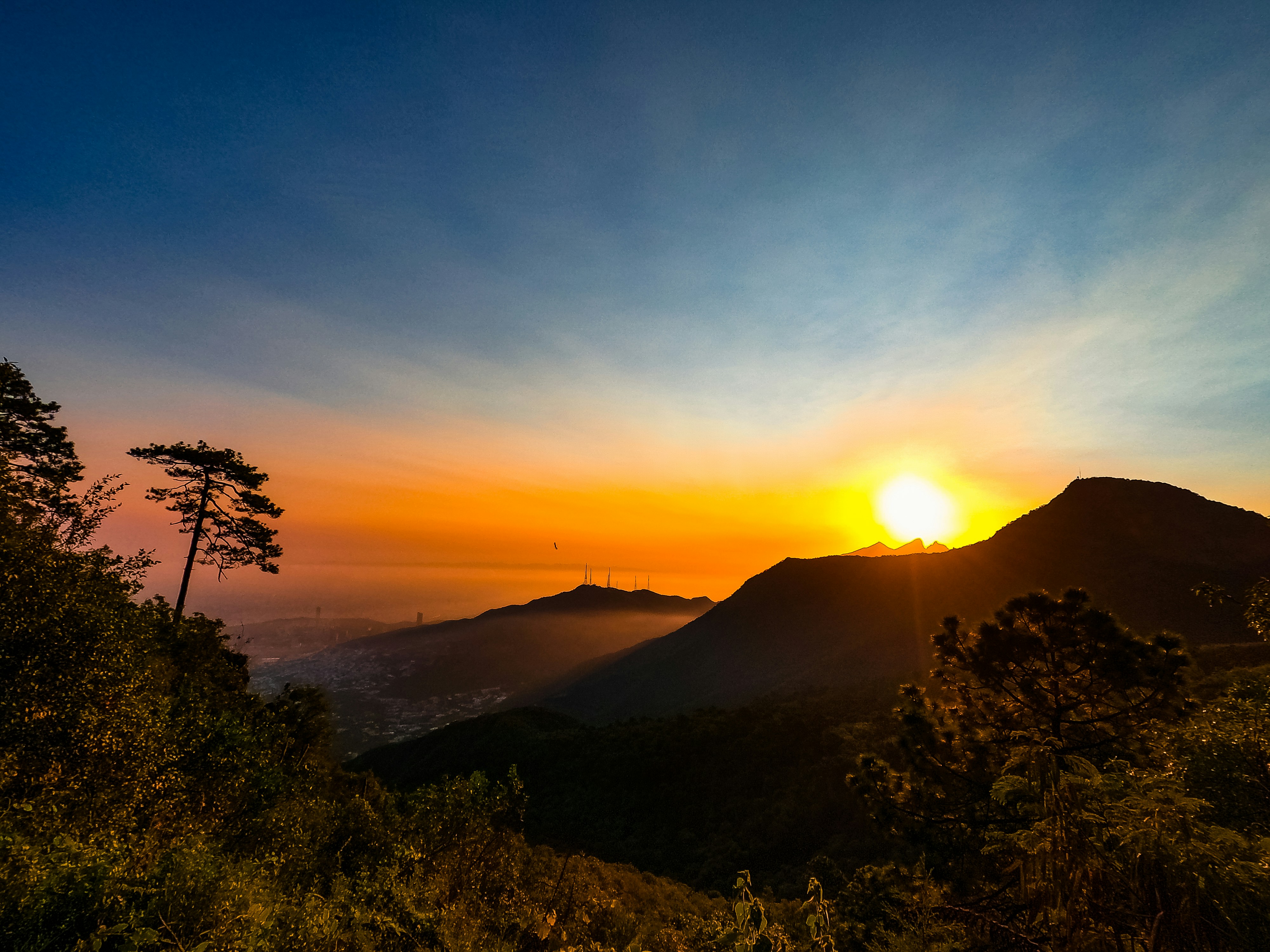 Sun rising over misty mountains with vibrant sky and silhouetted trees.