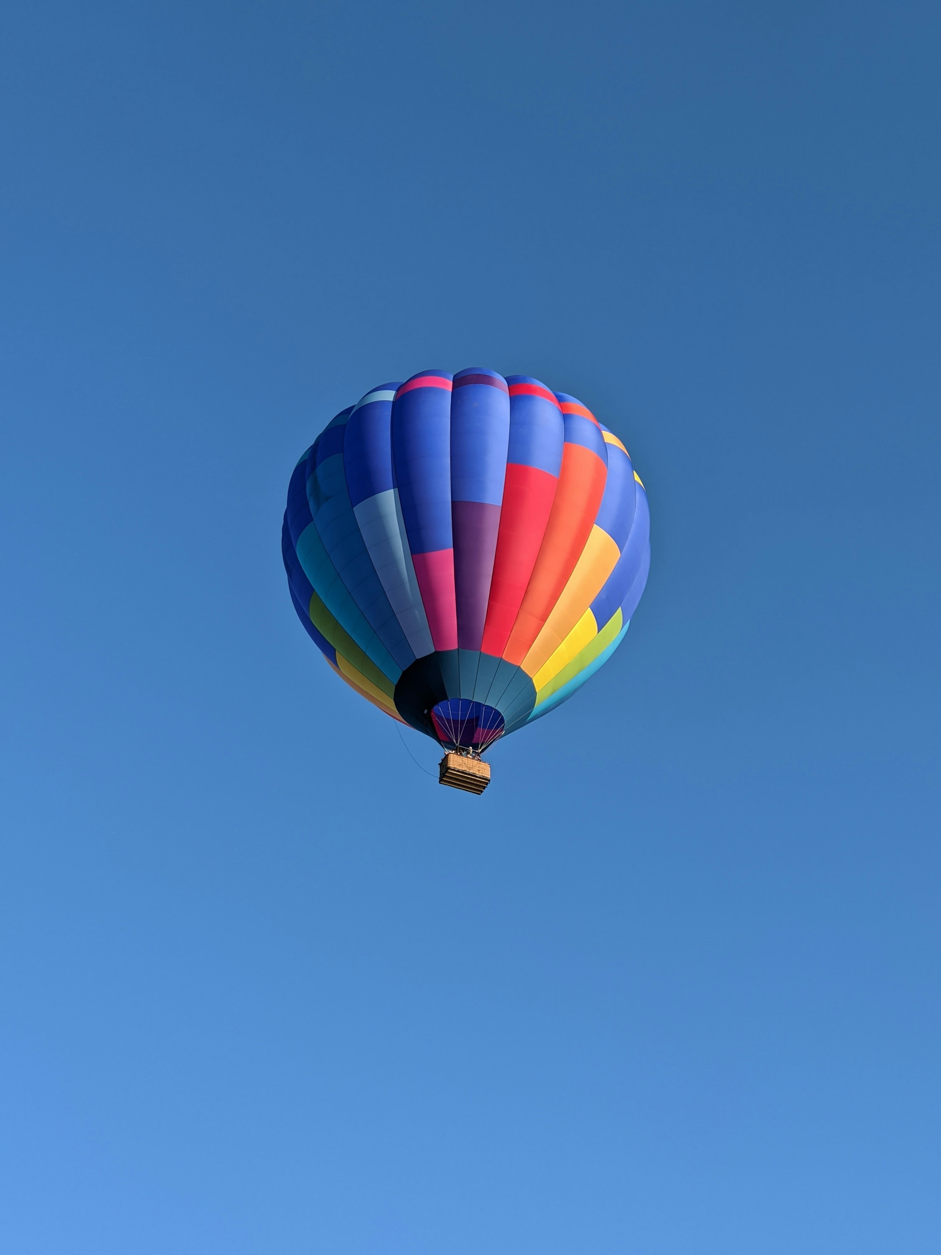 A vibrant hot air balloon floats against a clear blue sky, showcasing its colorful panels in full display.