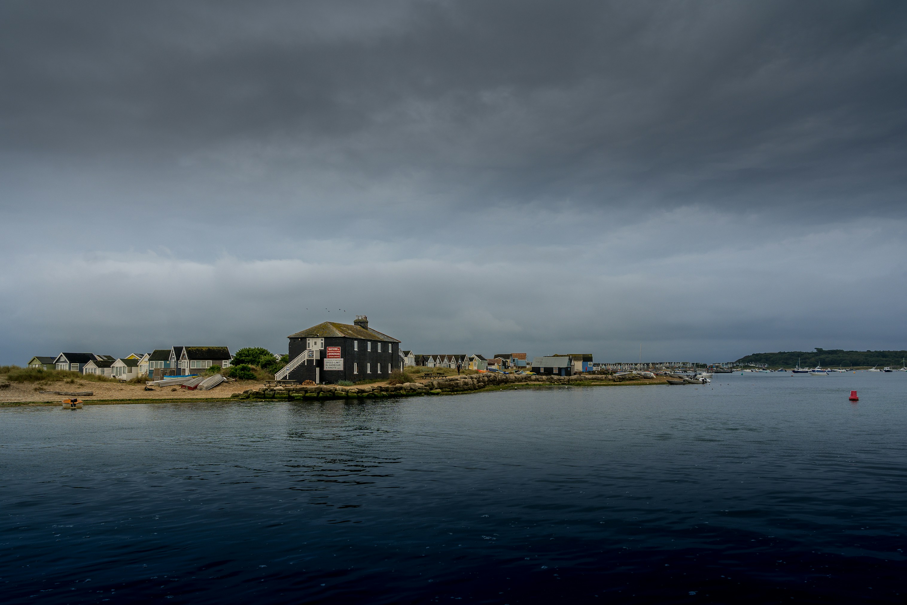 Dark clouds gather over Mudeford Spit and beach huts, signaling an impending summer storm.