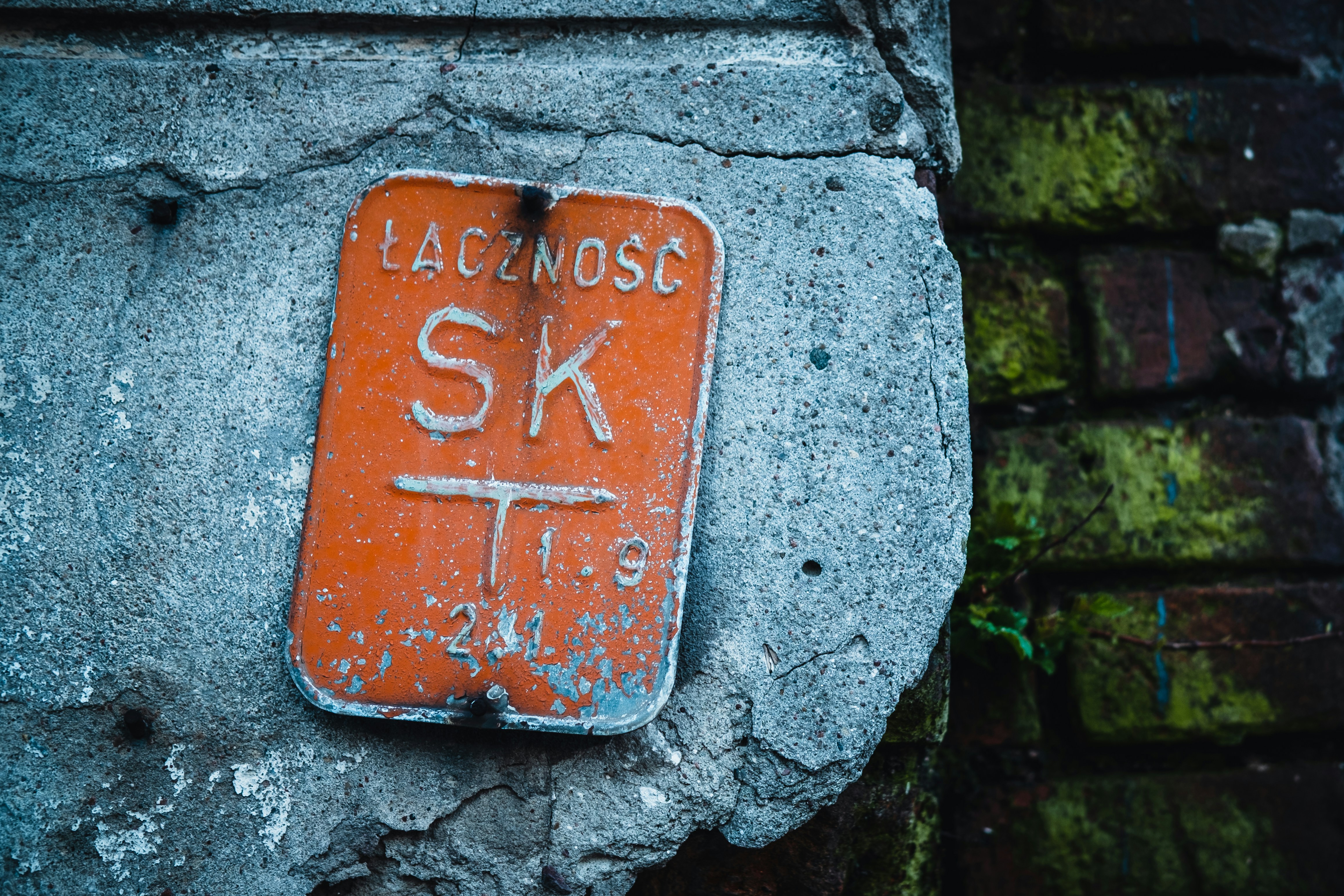 Weathered orange sign with faded white text mounted on a cracked wall, revealing remnants of history.