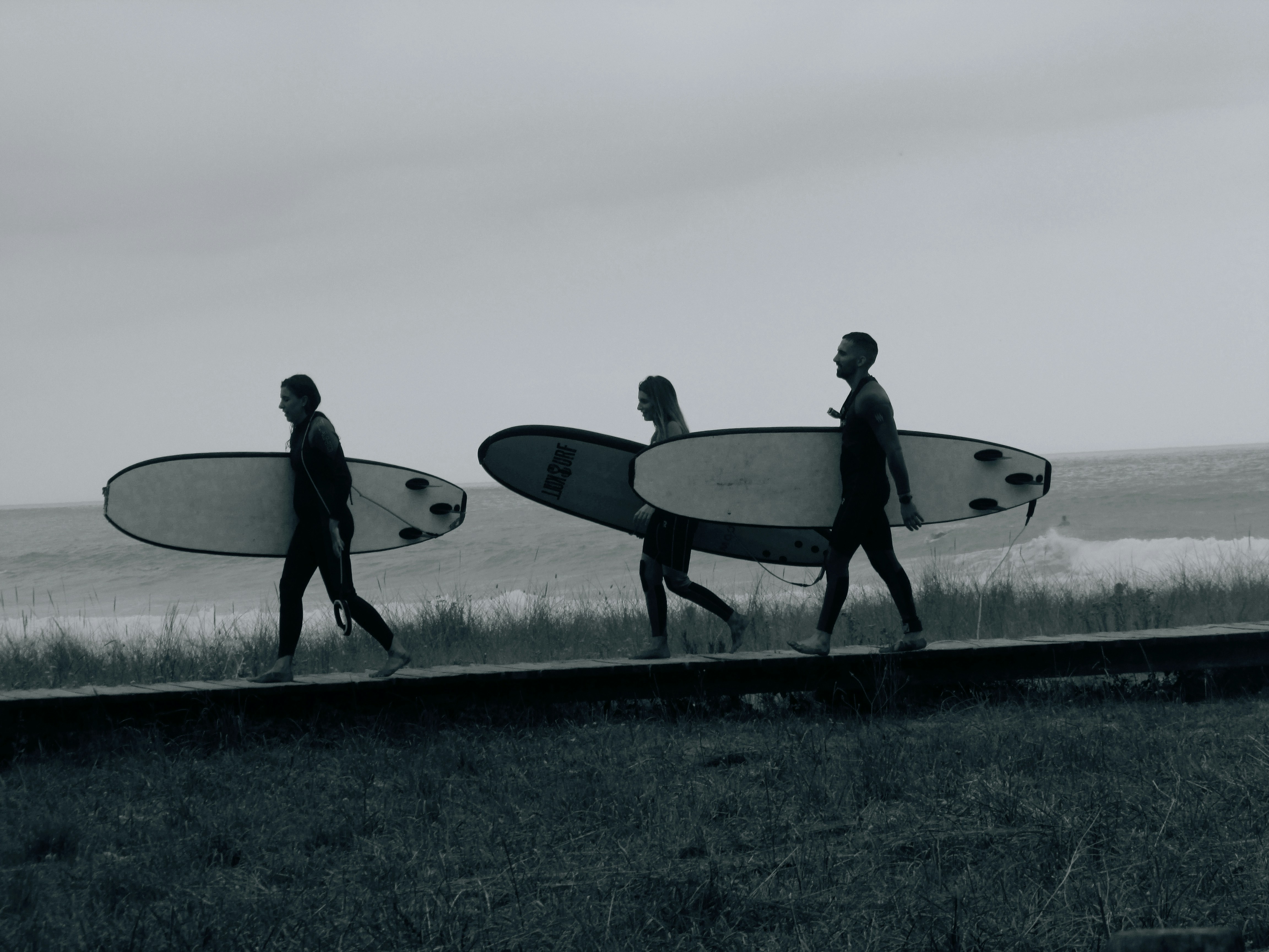 Triad of Silhouettes: Surfers Crossing a Quiet Coastal Walk