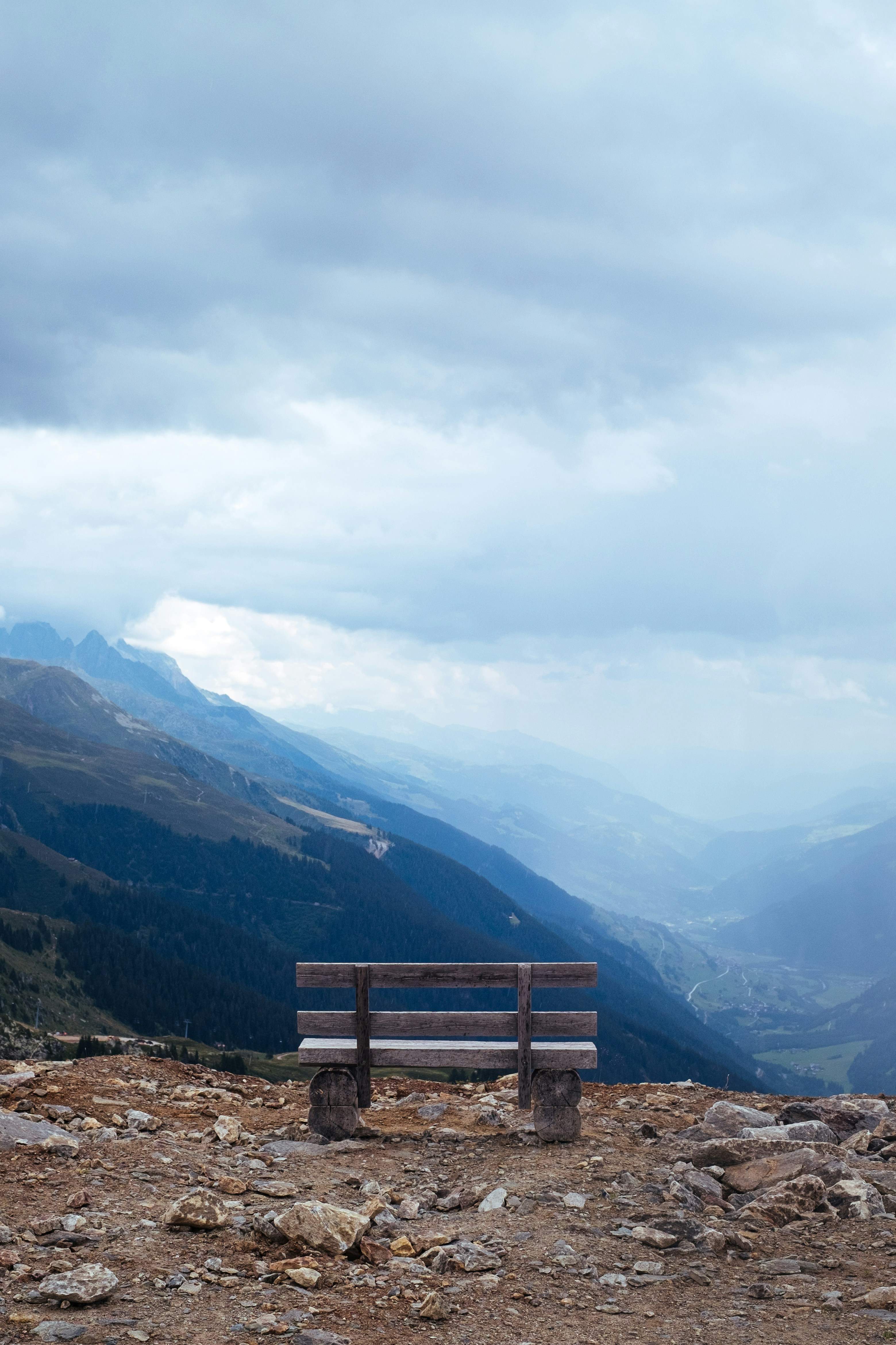 Wooden bench overlooking expansive mountain range and valleys under a cloudy sky.
