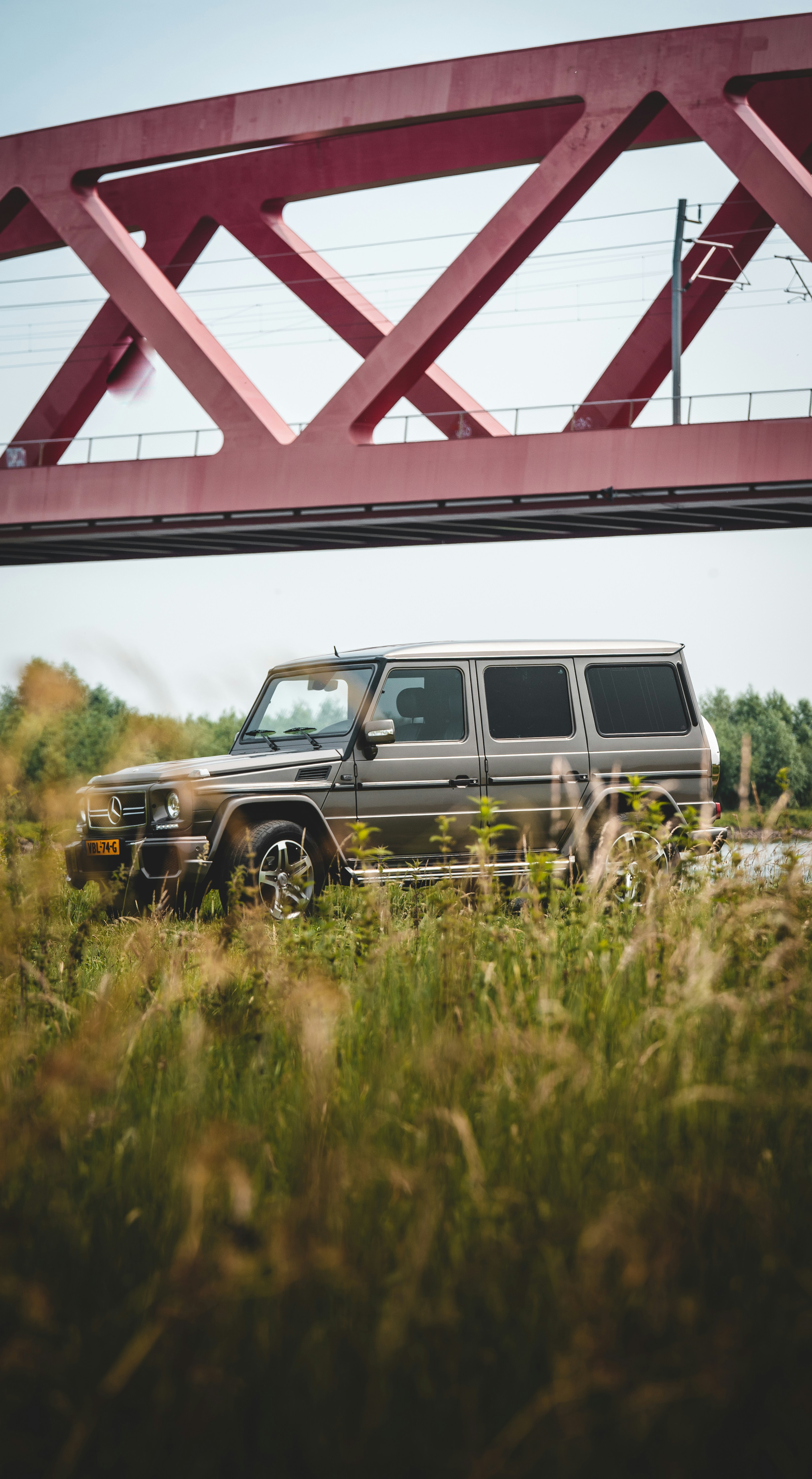 Gray Mercedes G-Wagen beneath a red truss bridge at golden-hour