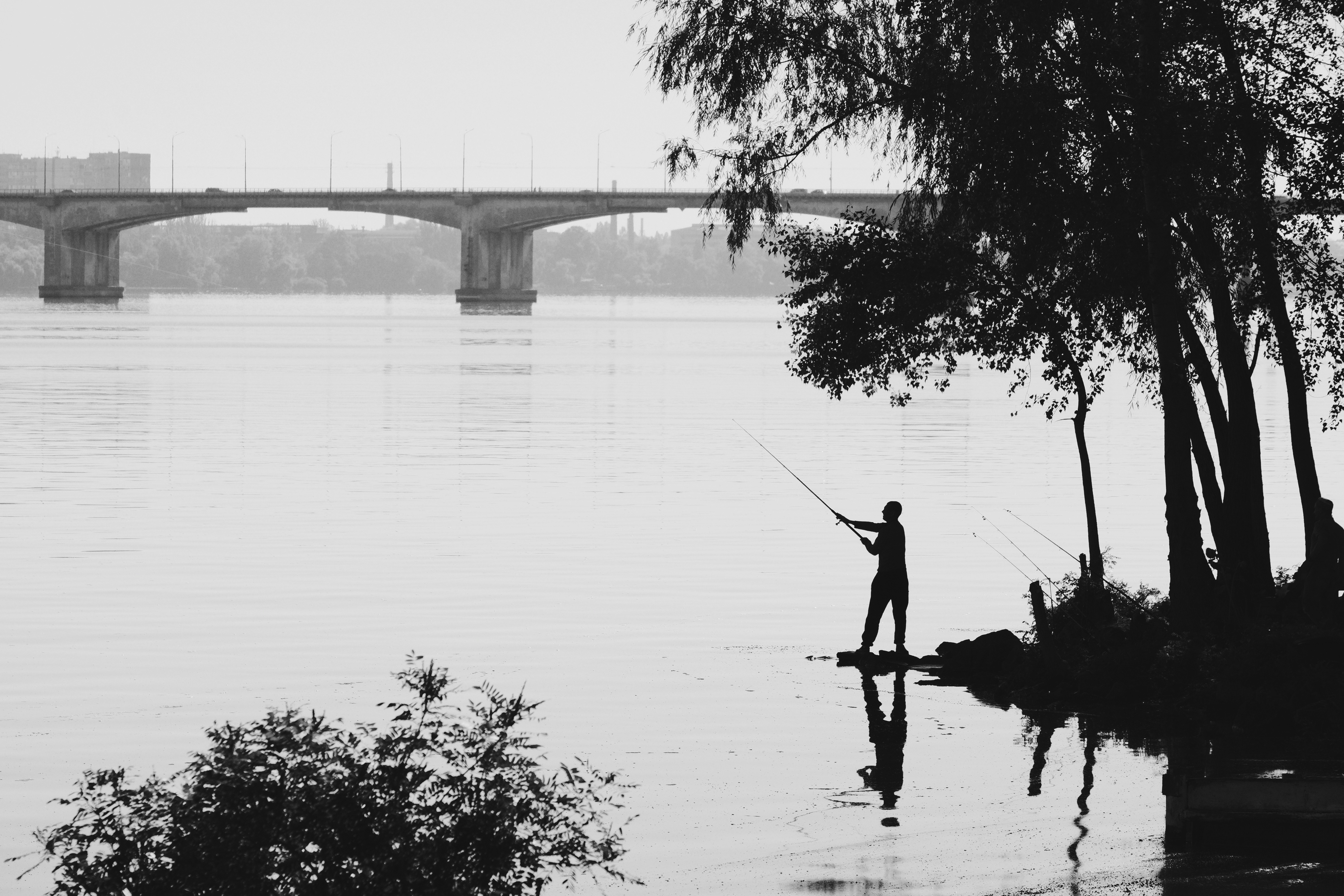 Silhouette Angler by the Quiet River: Casting Lines Under a Distant Bridge