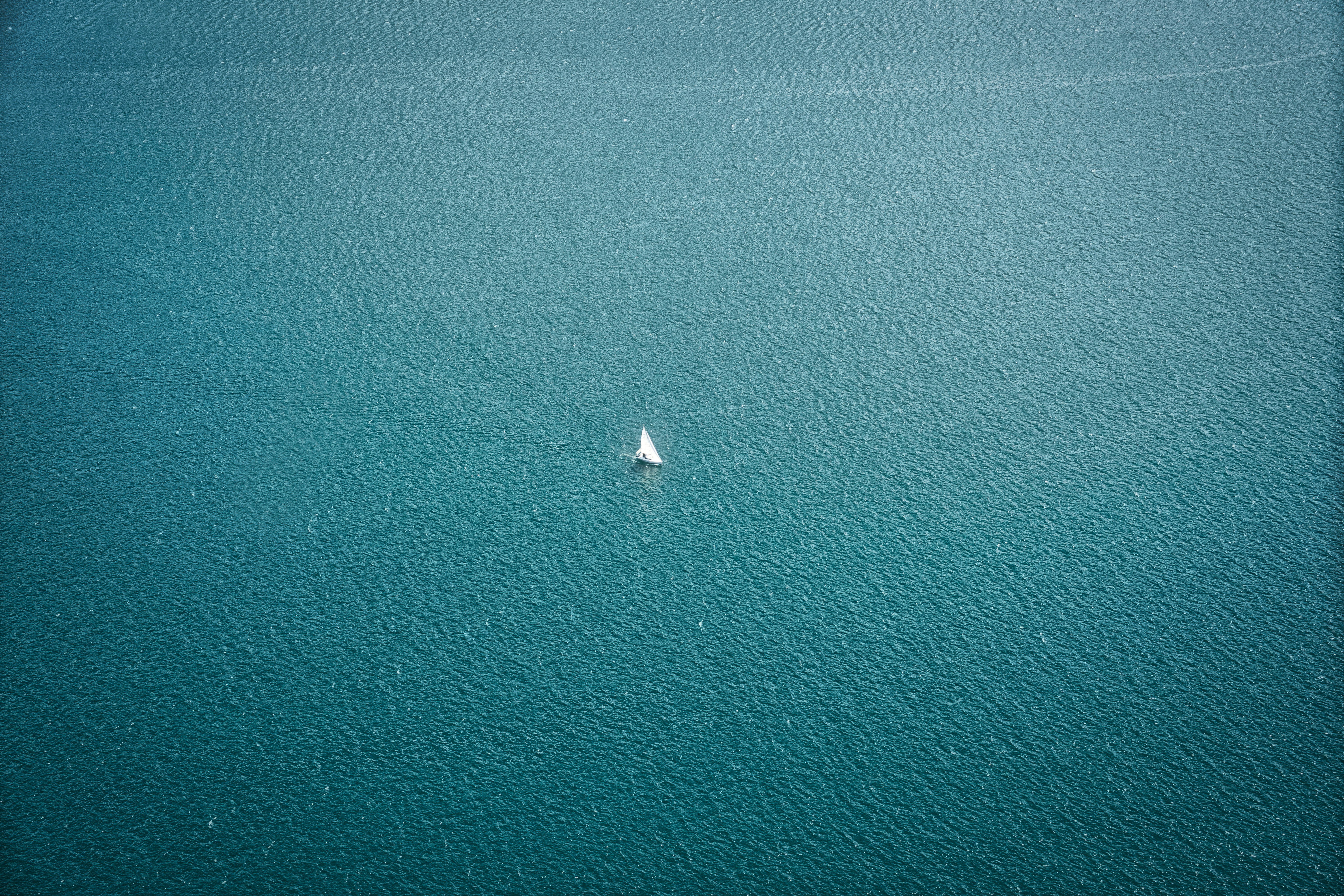 A single sailboat gliding across a vast expanse of tranquil blue water, creating a sense of solitude and peace.