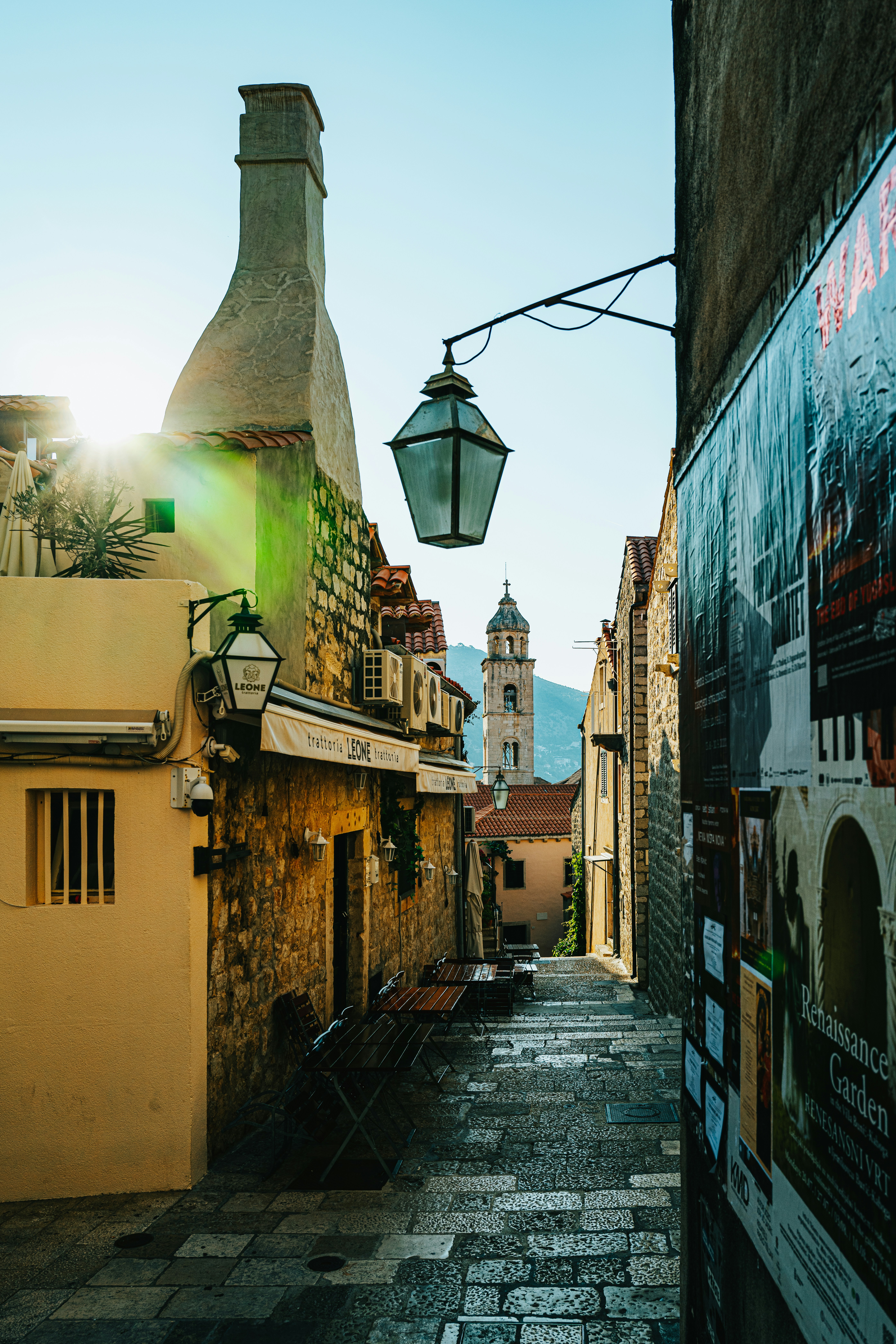 Sunlit Alleyway: Lanterns, Cobblestones, and a Distant Bell Tower