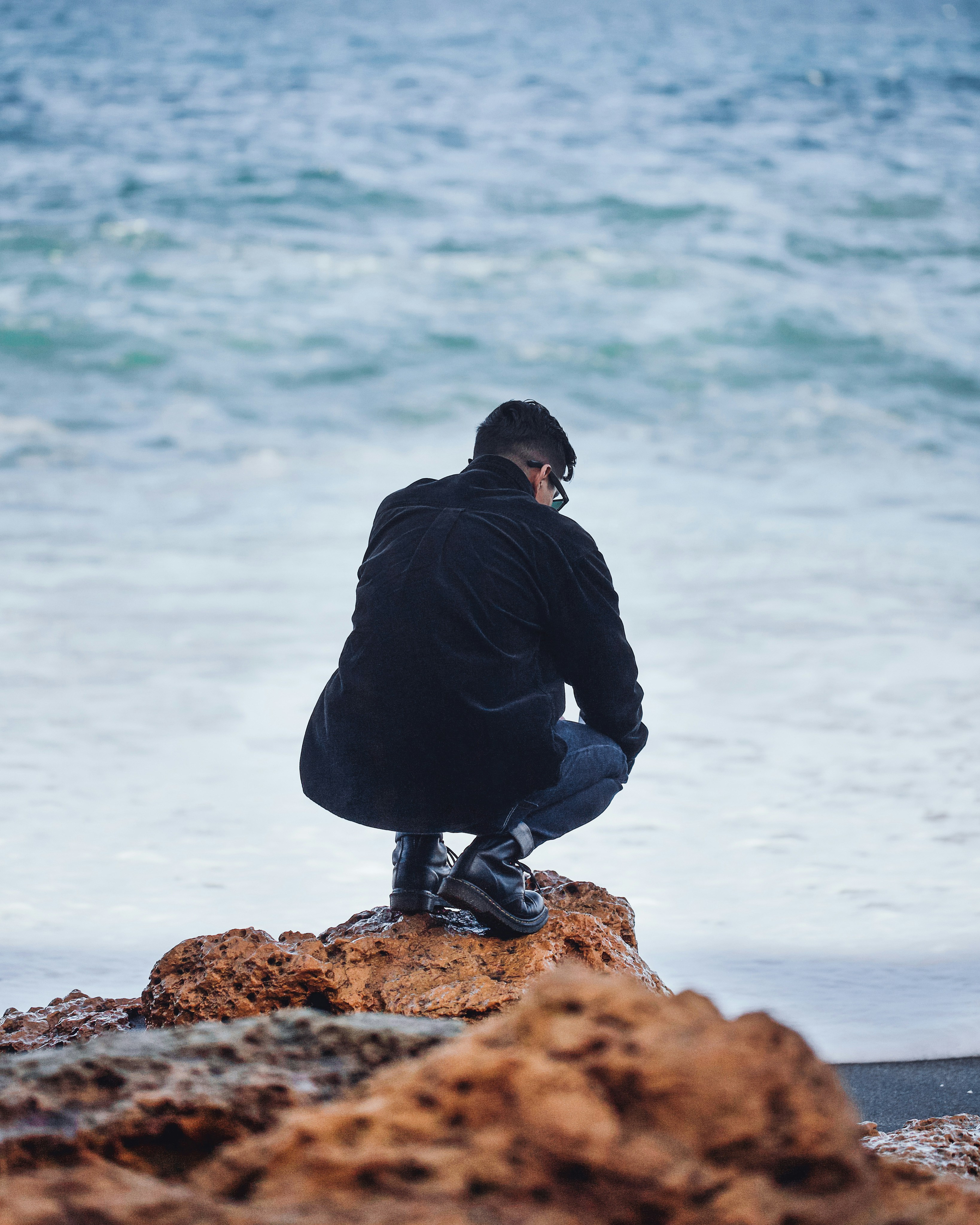 On the Edge of Quiet Blue: A Seaside Figure on Weathered Rocks