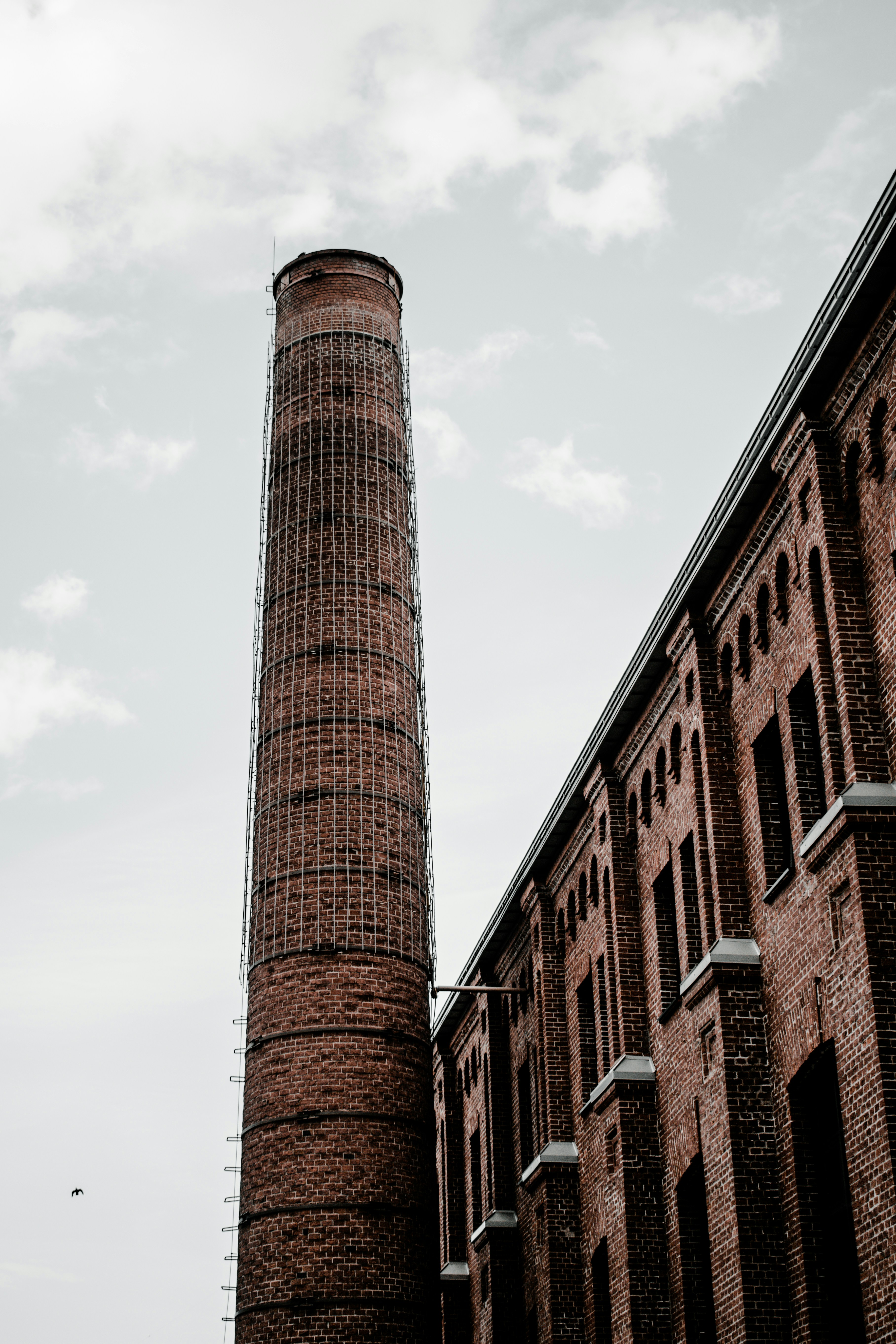 A tall, brick smokestack rises against a cloudy sky, showcasing the architectural remnants of an industrial era. The adjacent building's intricate details complement the structure's historical significance.