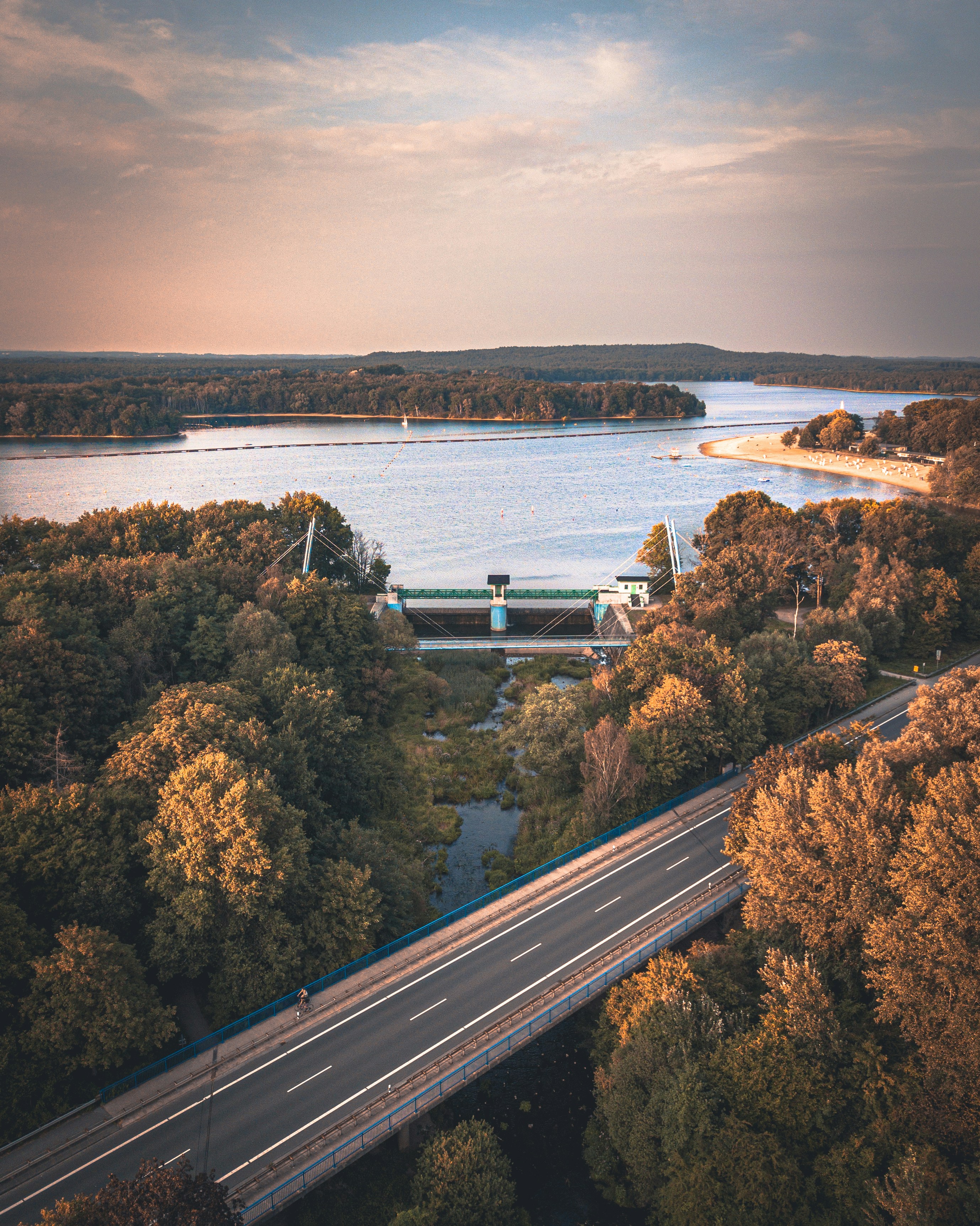 Aerial view of a winding river bordered by lush trees and a roadway, capturing the tranquil essence of nature at dusk.