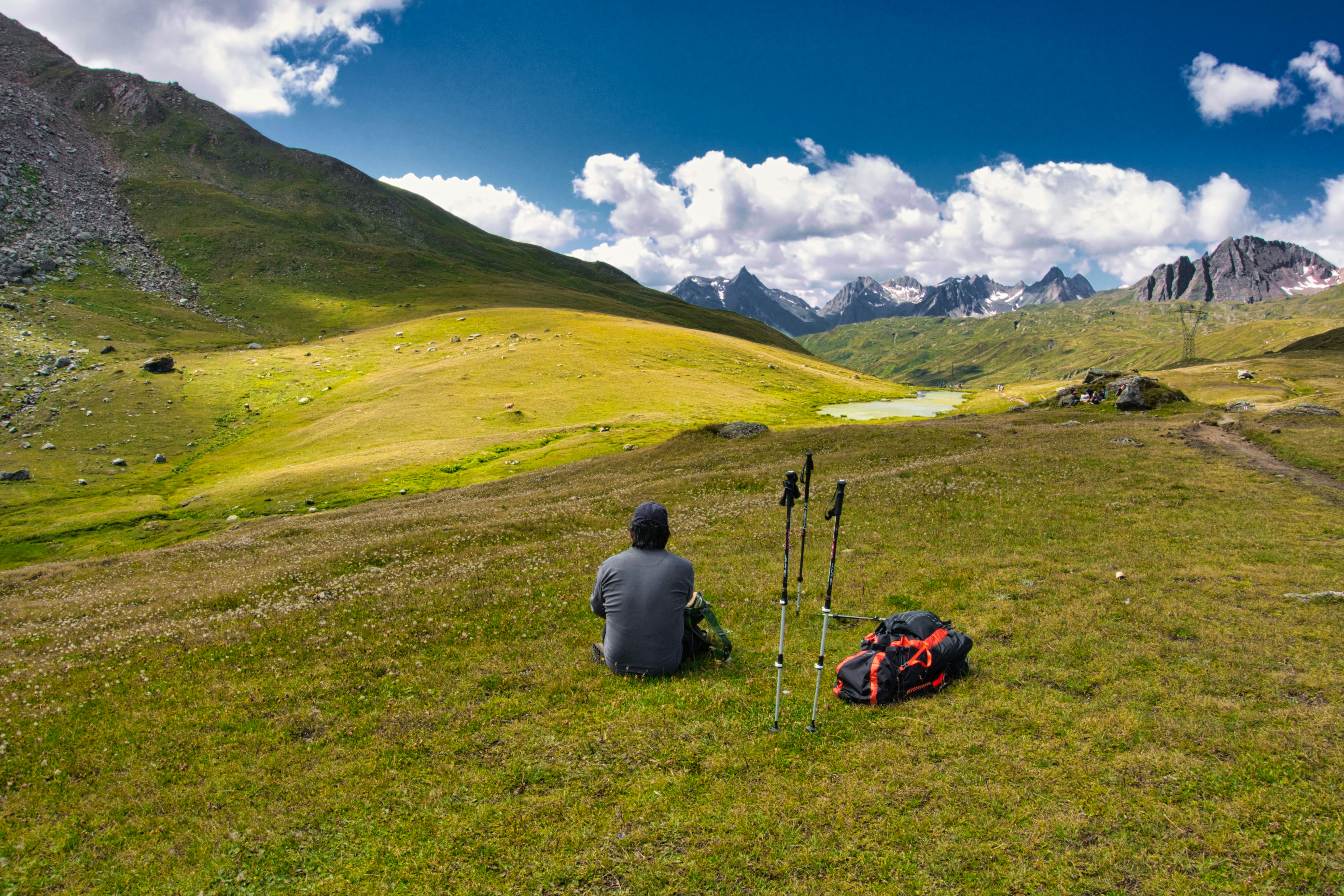 Alpine Pause: A lone hiker rests on sunlit meadow beneath jagged peaks