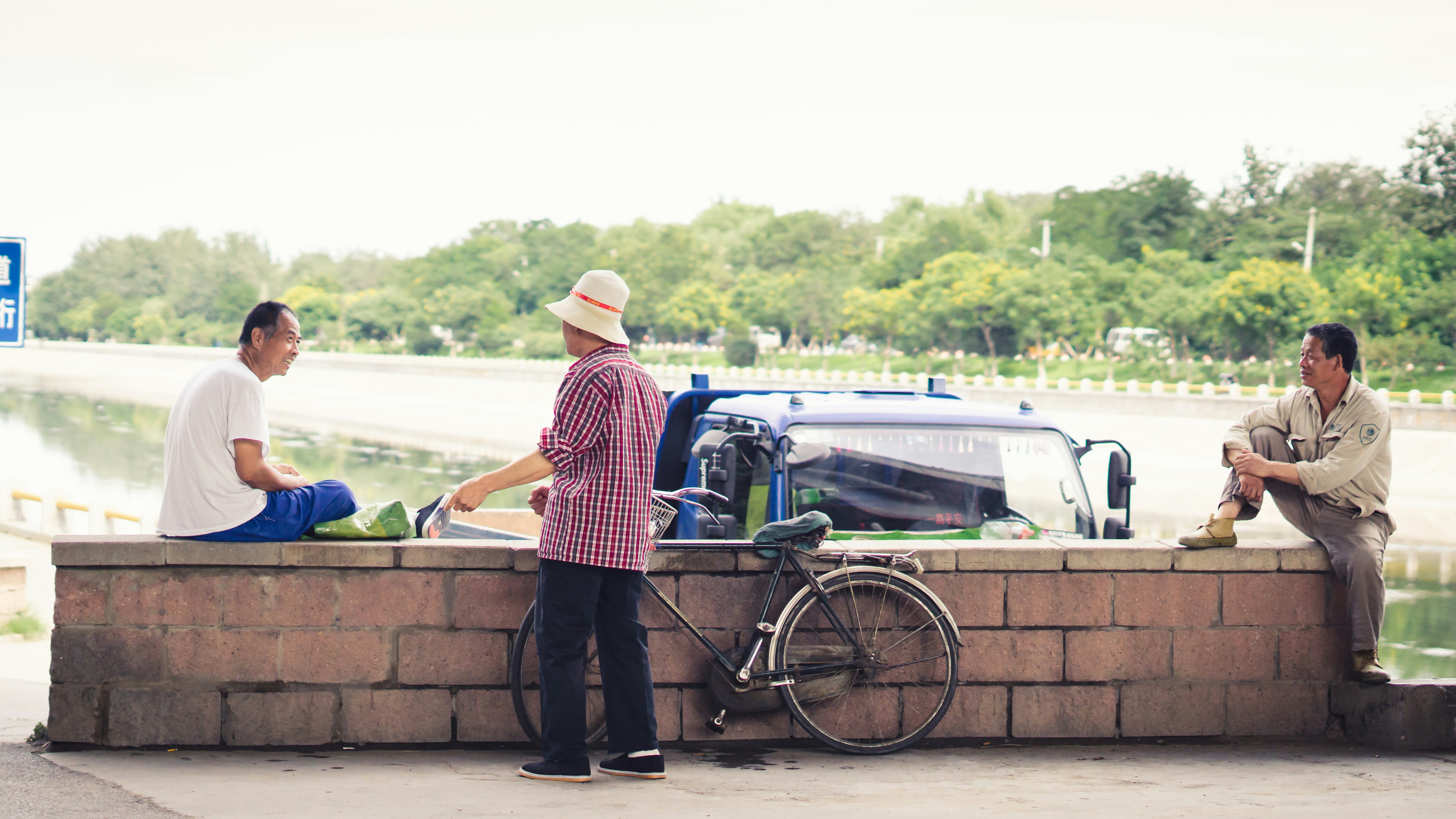 Riverside Convergence: Hat, Bicycle, and Conversation by the Wall