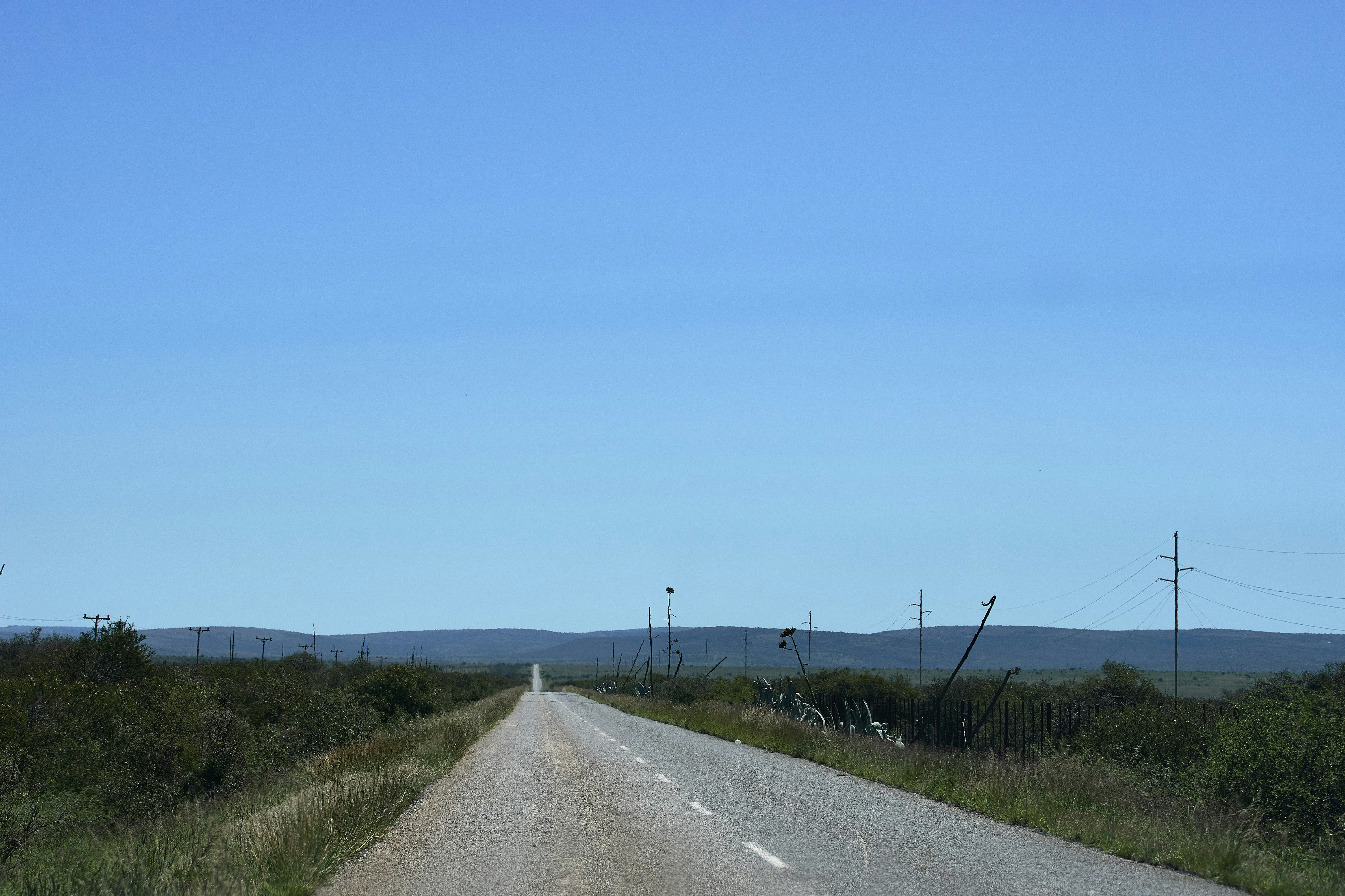 gray concrete road between green grass field under blue sky during daytime