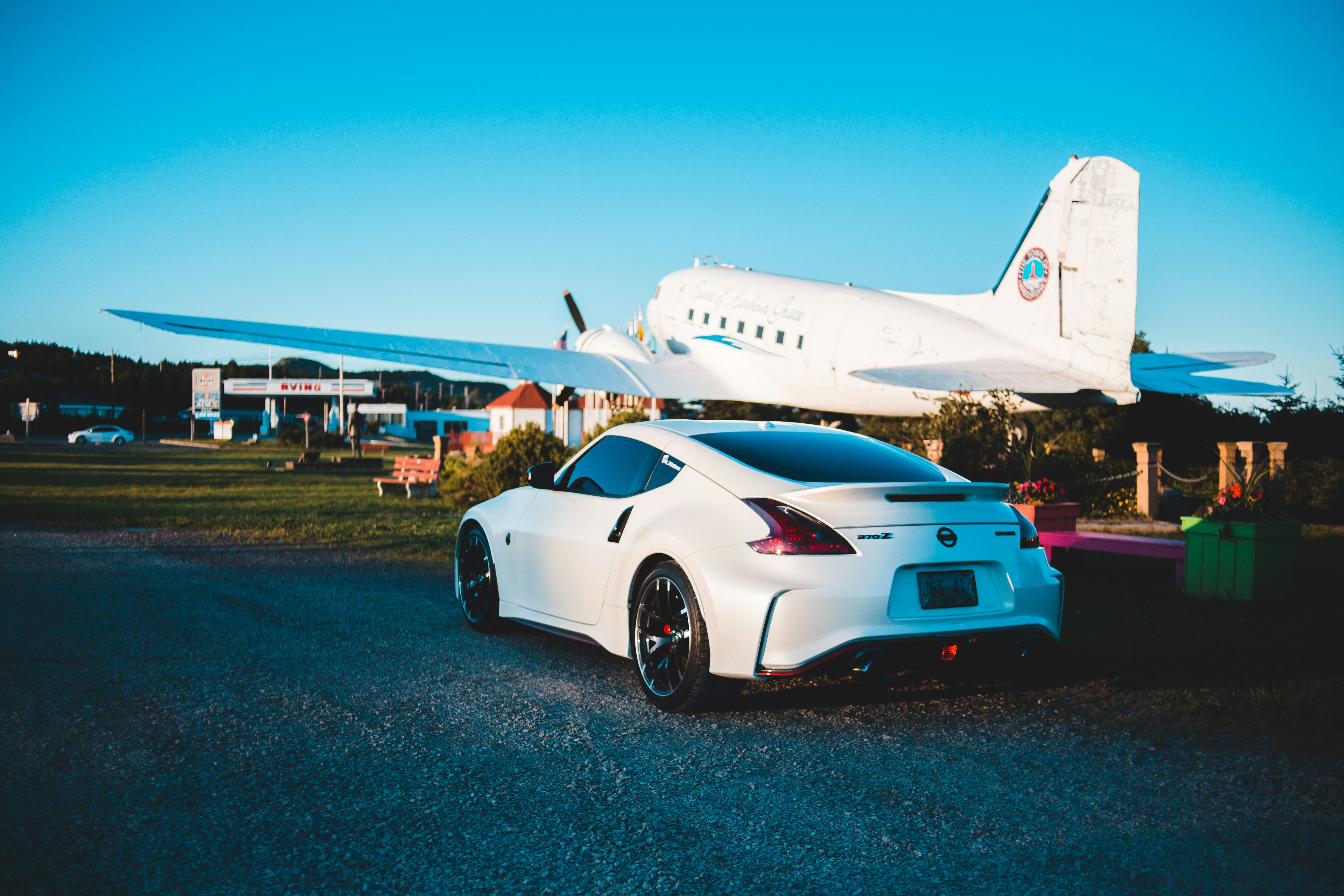 White sports car under a vintage aircraft at a bright airfield